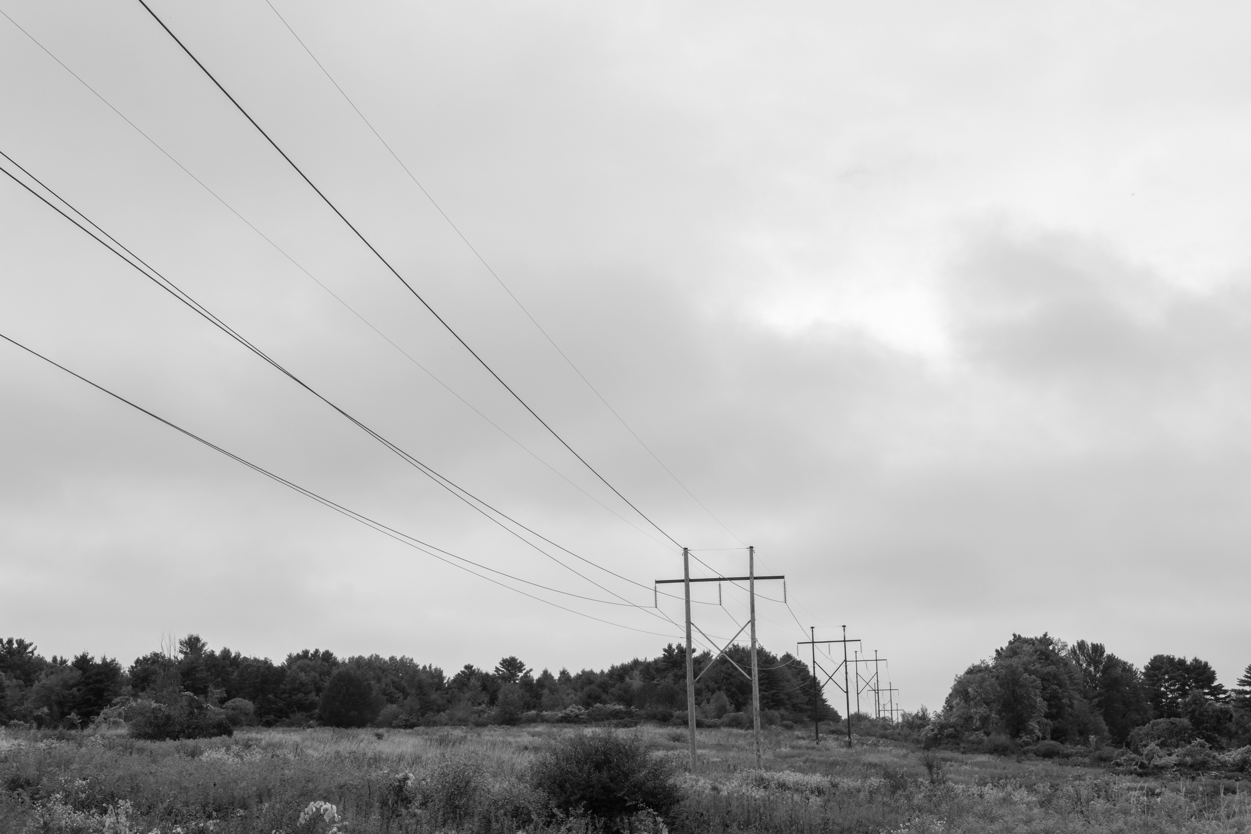 Power lines stretch across a grassy hill under cloudy sky.
