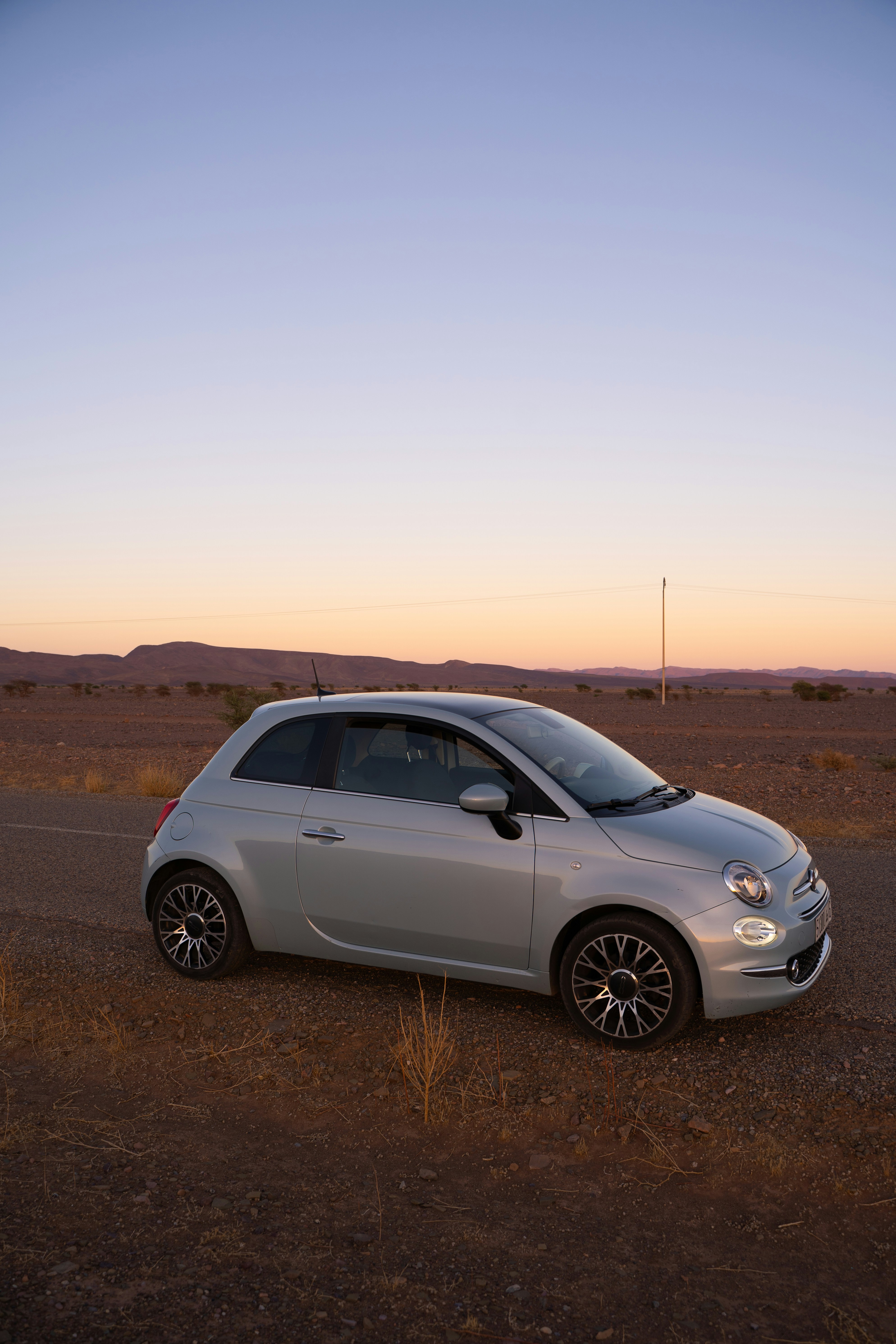 A sleek silver car parked on a deserted road, framed by a vast, arid landscape under a soft twilight sky.