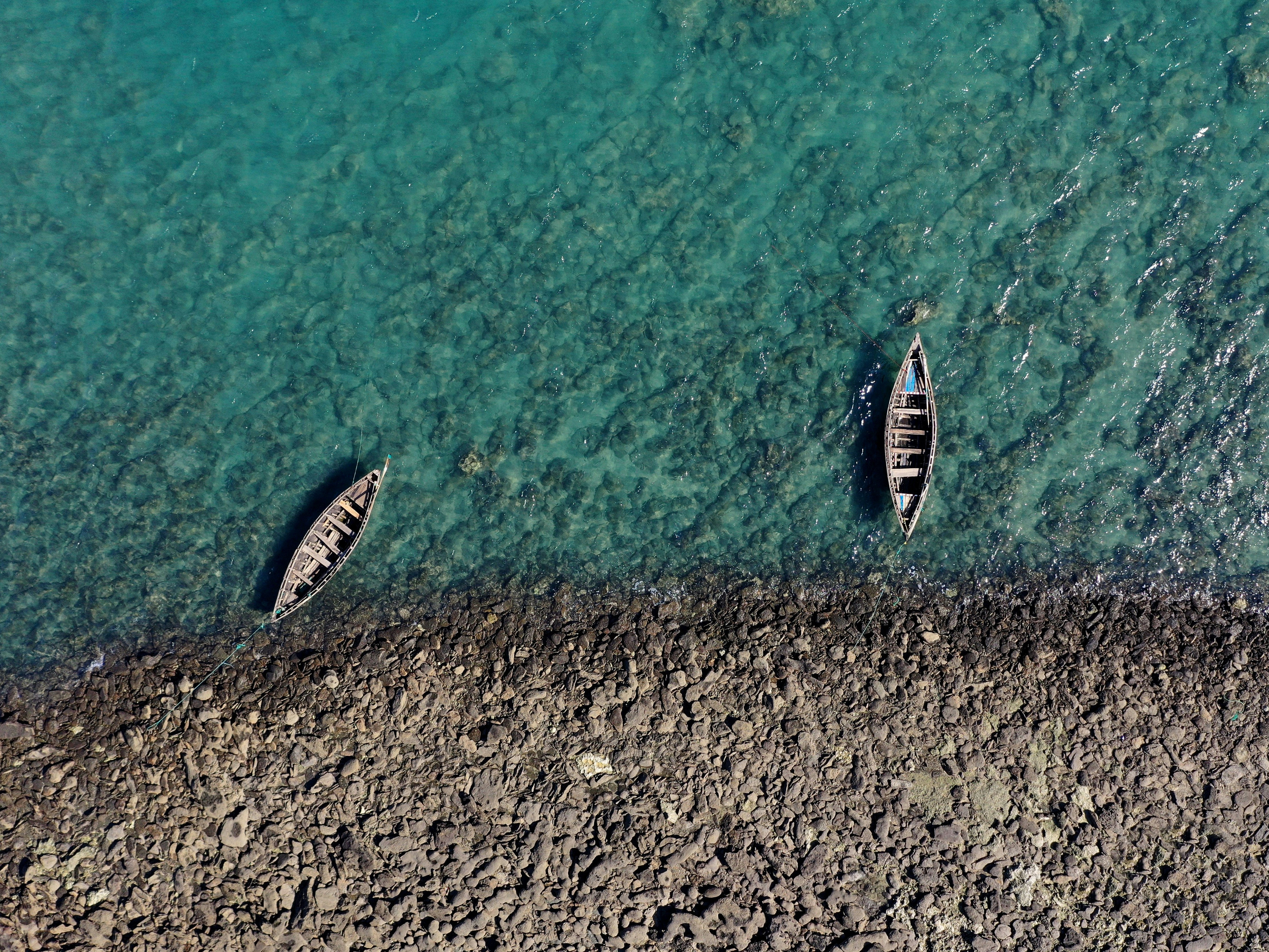 Aerial view of two wooden boats floating near a rocky shoreline in clear turquoise water, capturing the beauty of nature, calmness, and traditional river life.