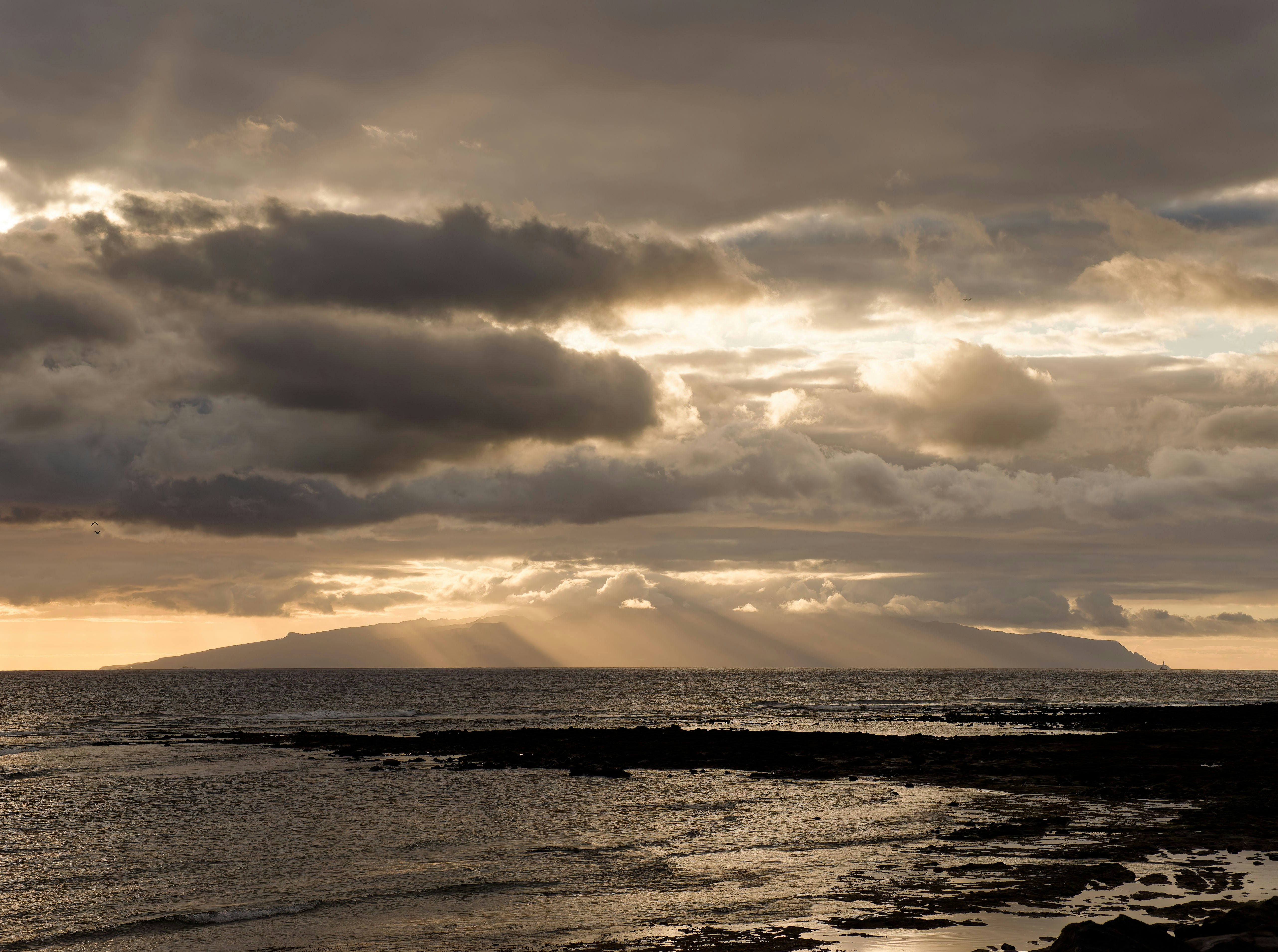 Sunbeams breaking through clouds over ocean and island.