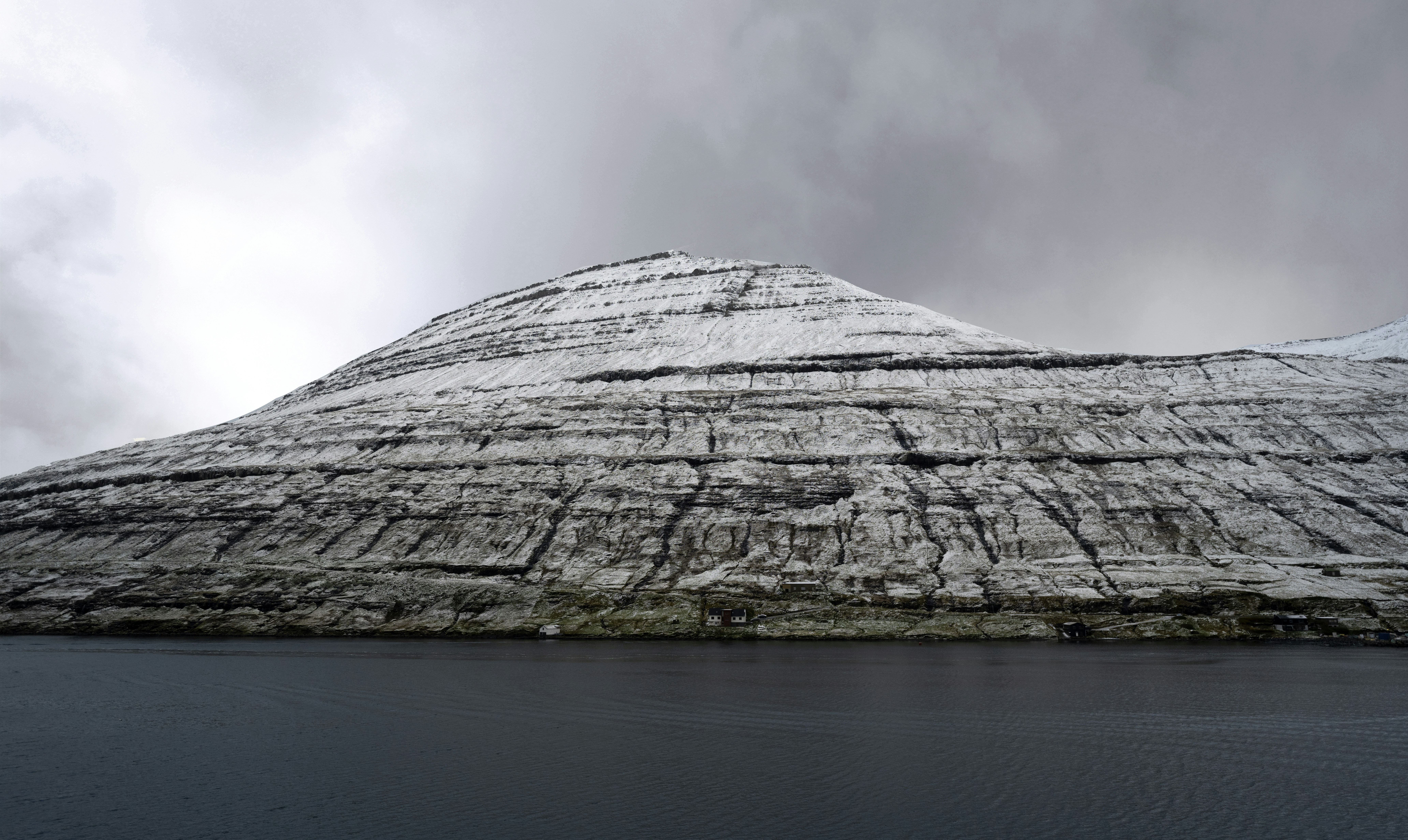 Snow-covered mountain slope above dark water
