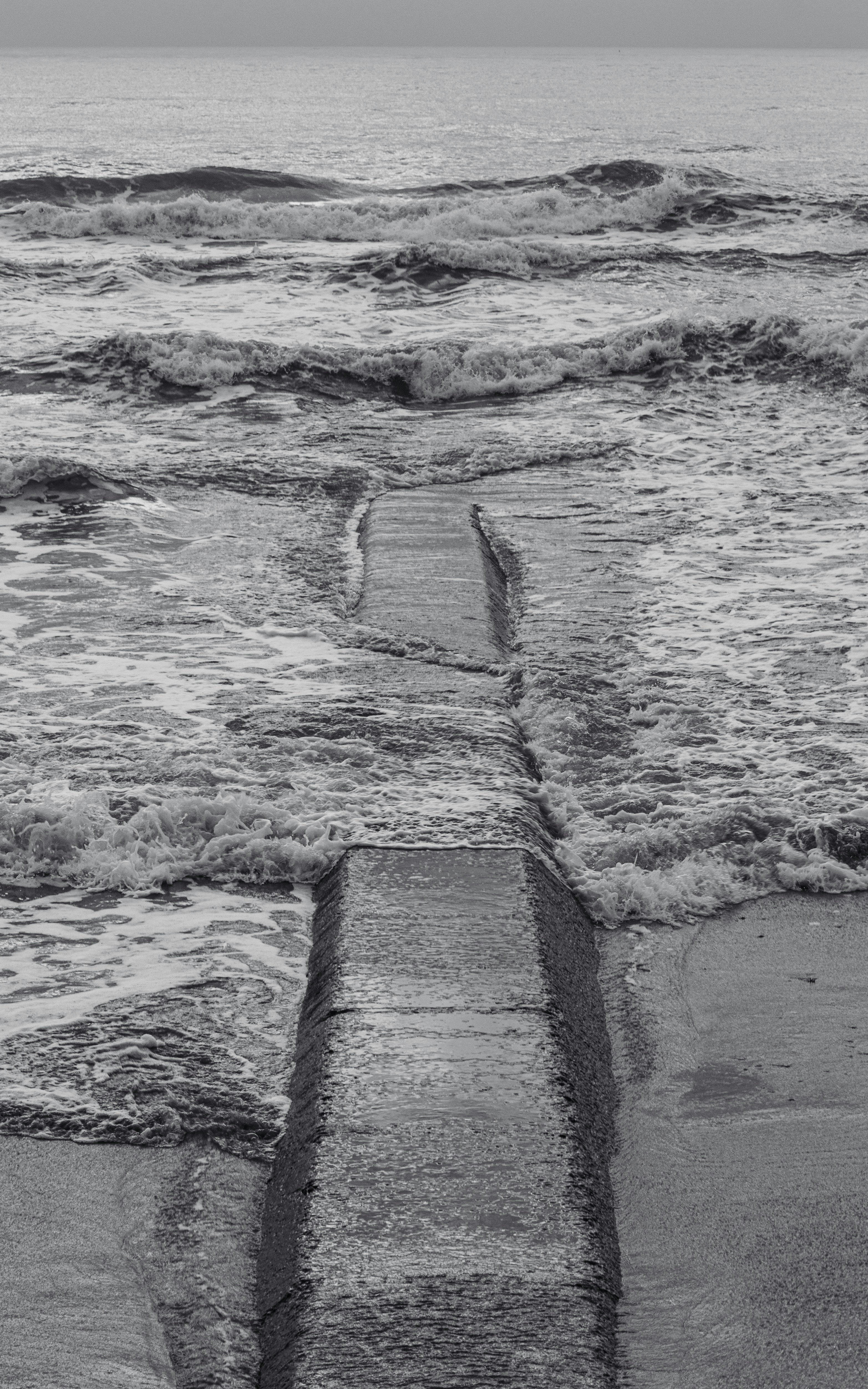 Concrete pathway leading into the ocean, partially submerged by waves, creating a dynamic interplay of water and structure.