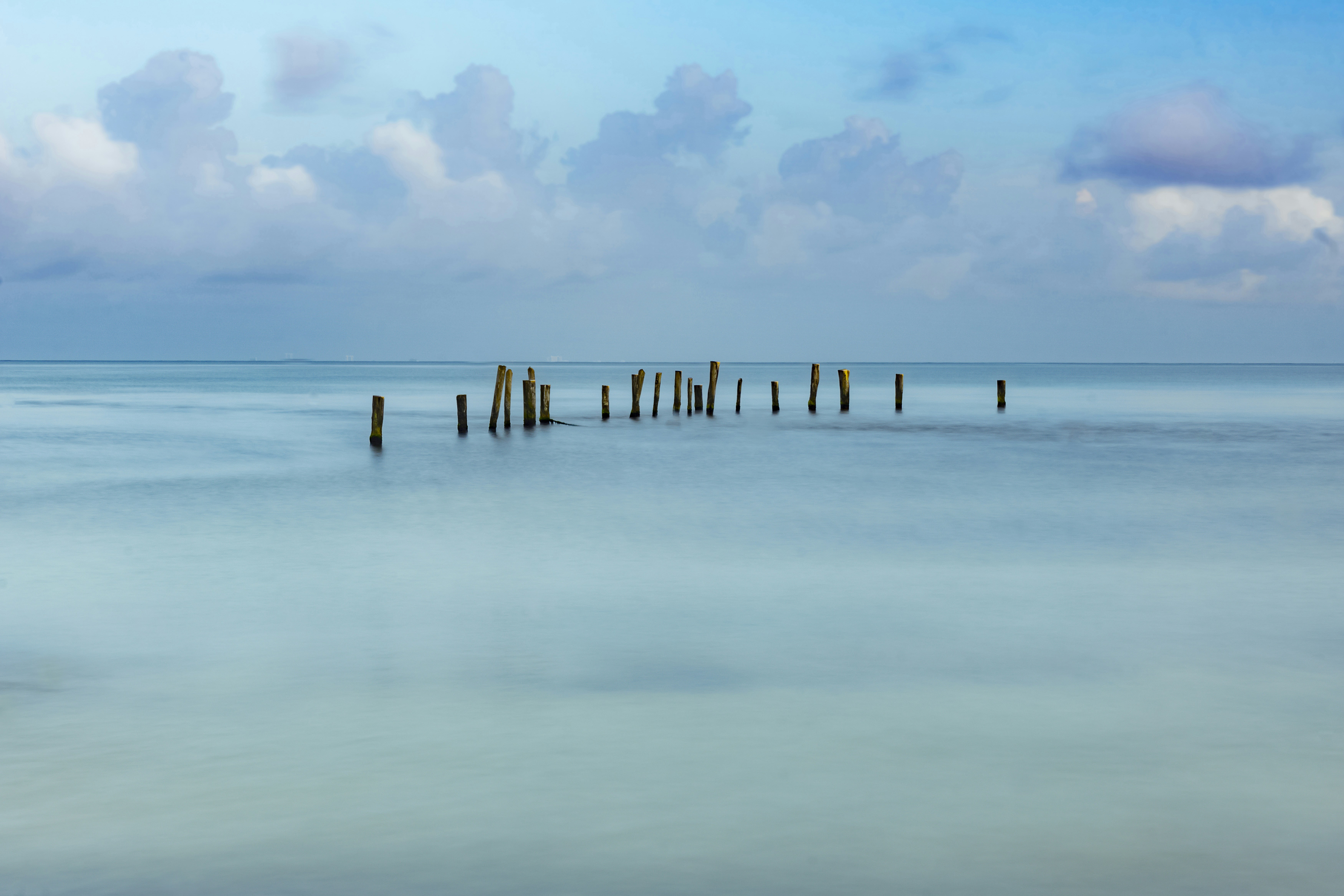 Pilings in a calm ocean under a cloudy sky