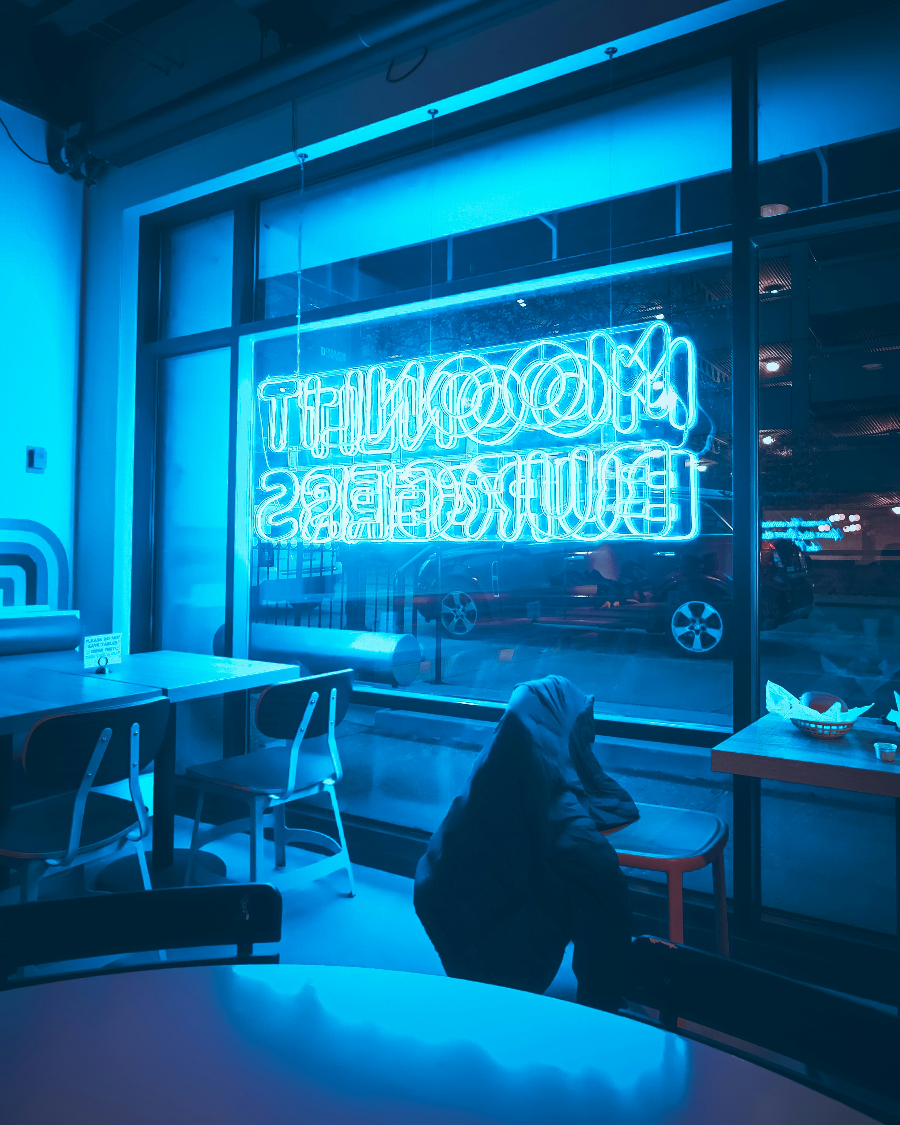 Person sitting in dimly lit cafe with neon sign.