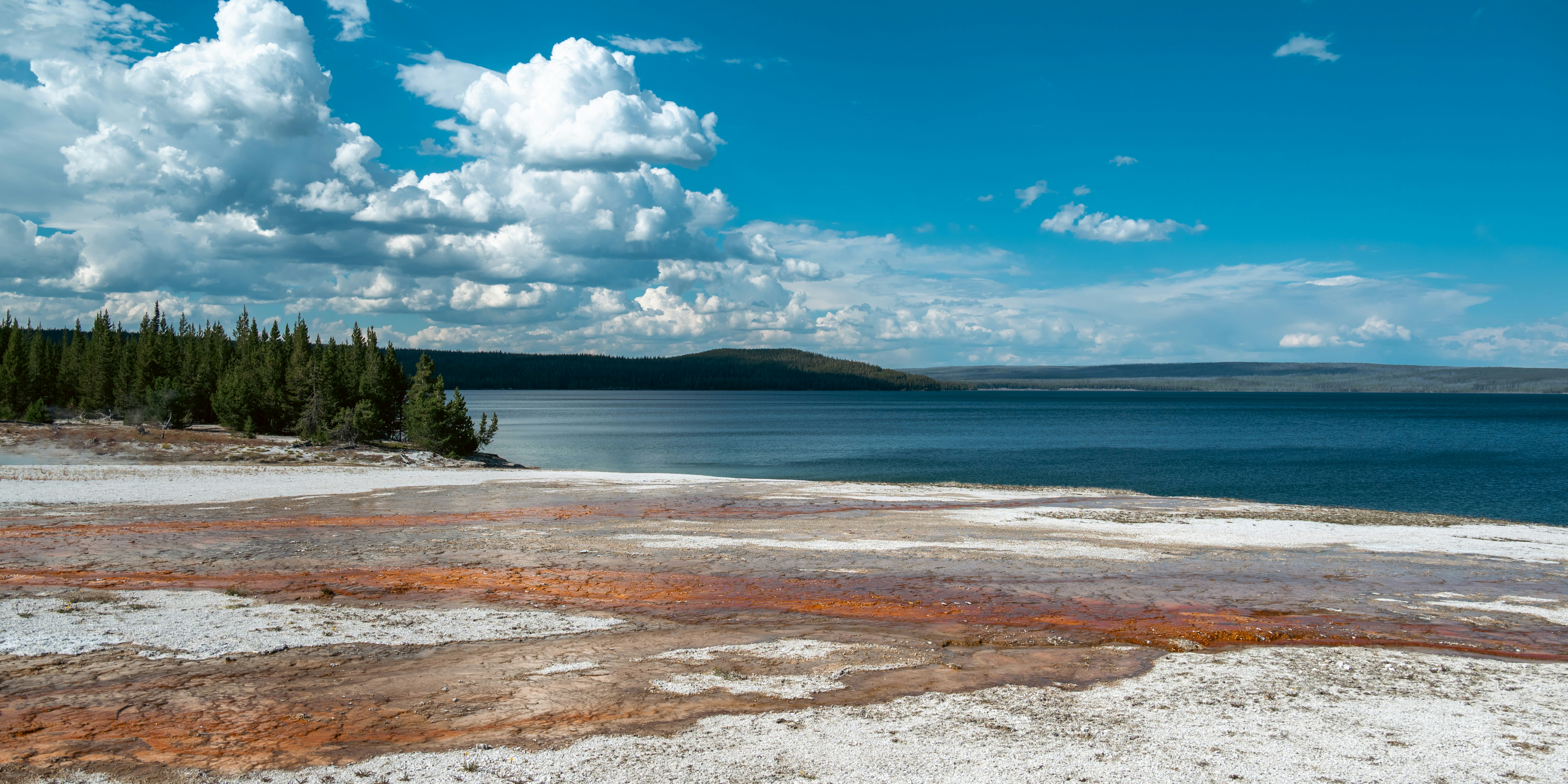 Vibrant geothermal features meet a tranquil lake under a dynamic sky, showcasing the beauty of Yellowstone National Park.
