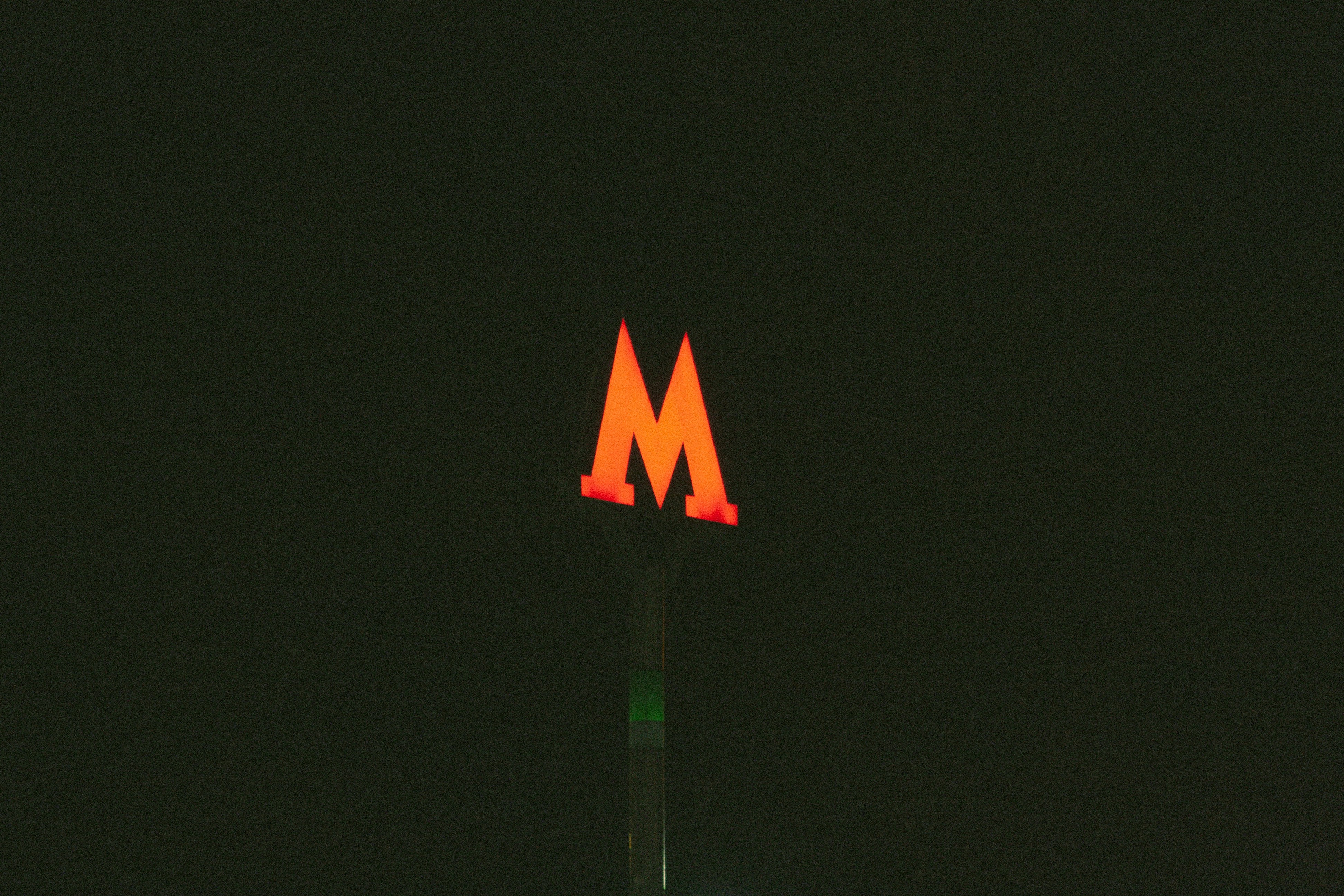 Glowing orange letter m sign at night.