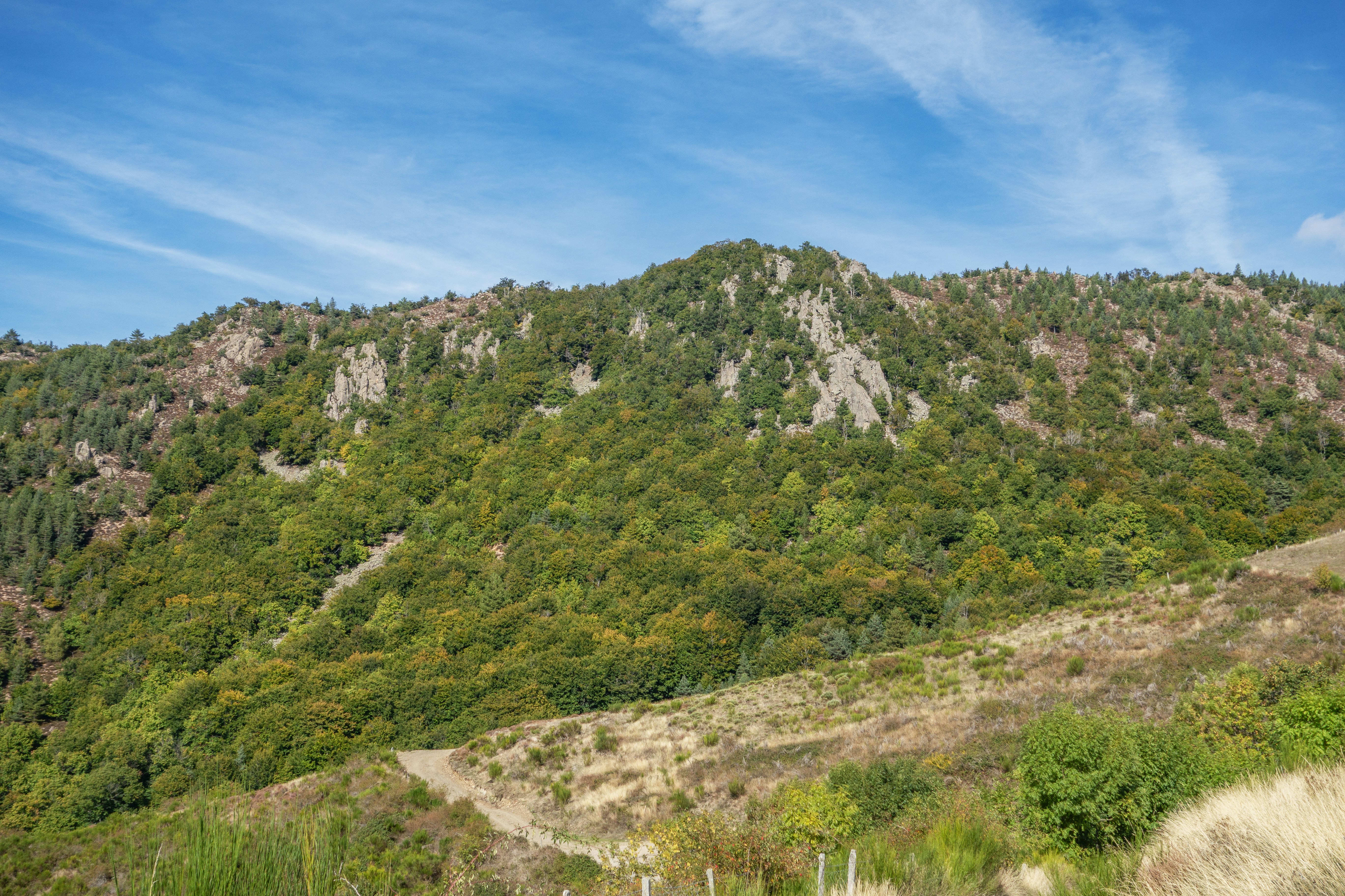 Lush green hills adorned with rocky outcrops stretch under a bright blue sky, showcasing the beauty of nature's palette.