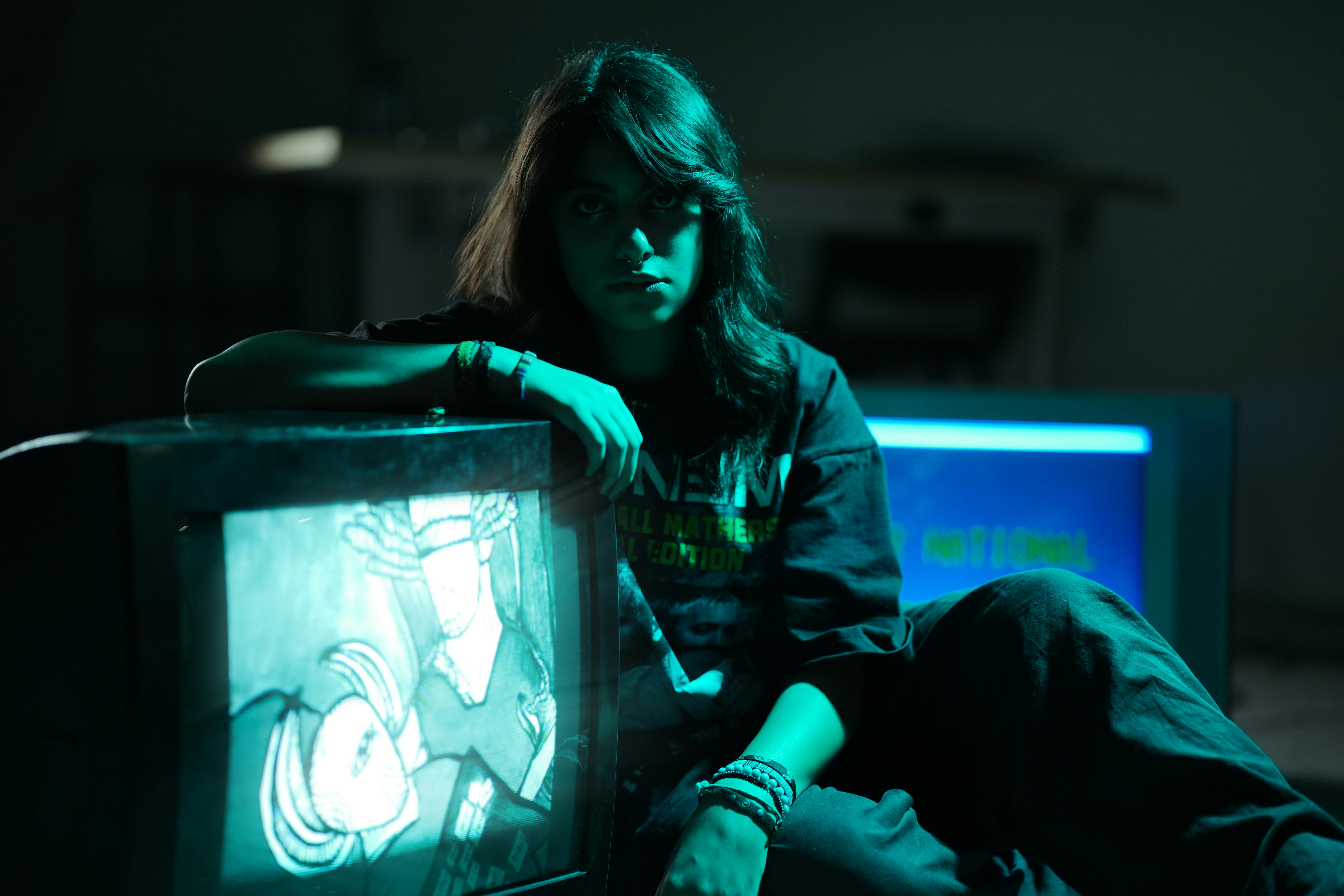 A young person sits beside vintage televisions, illuminated by their glowing screens, creating a nostalgic yet eerie atmosphere.