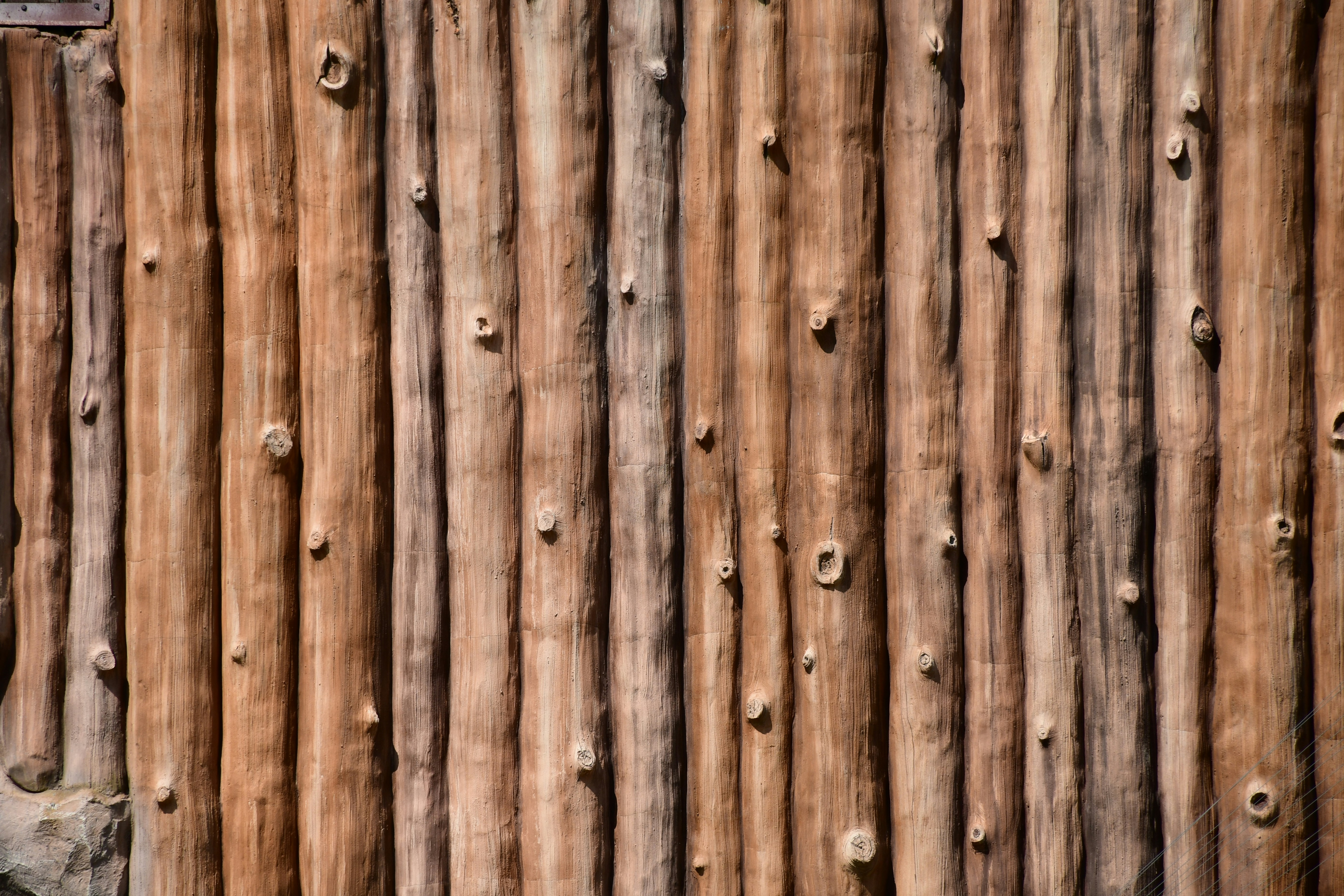 Vertical wooden logs with knots form a textured wall.