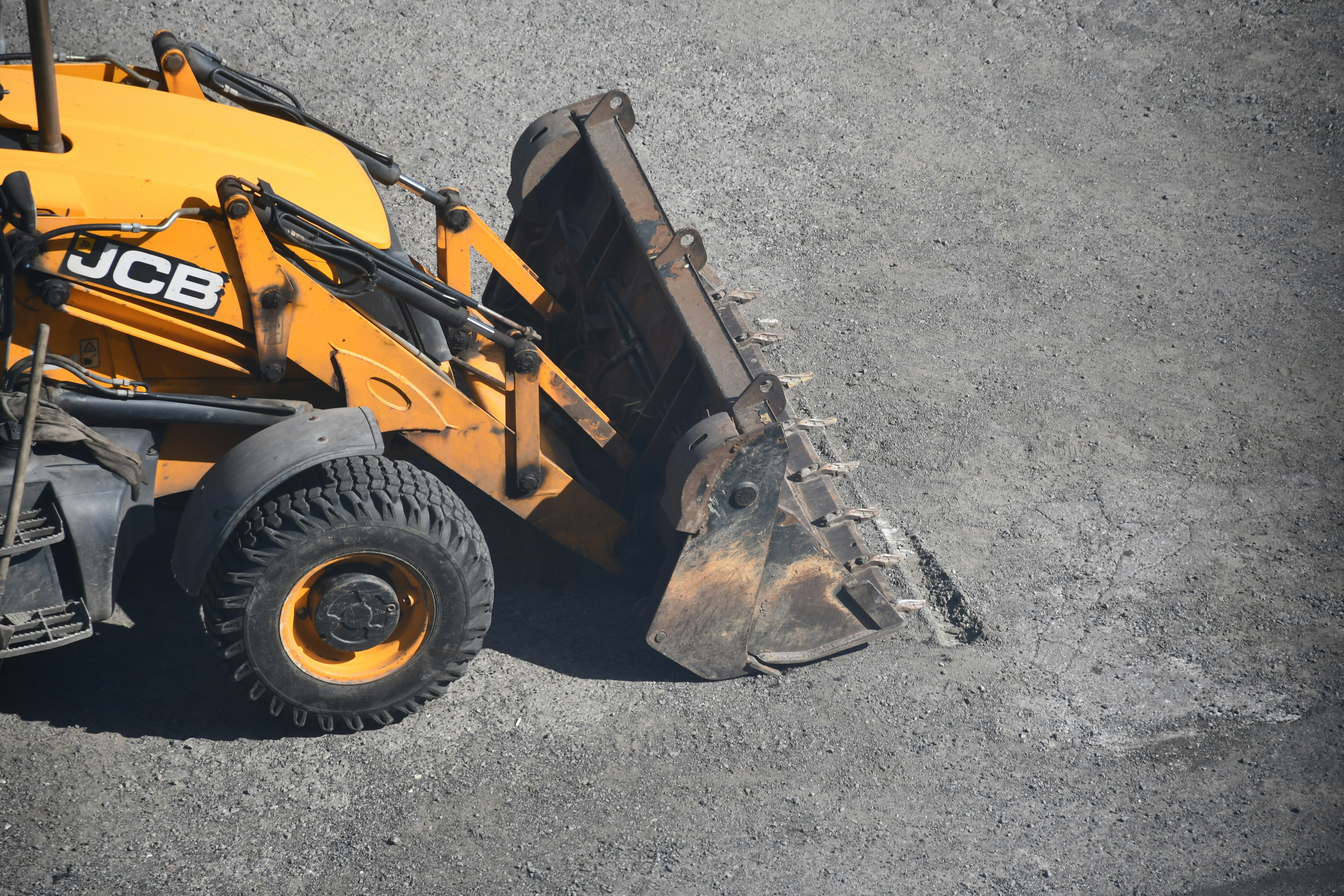 Yellow backhoe loader digging into gravel photo – Free Development ...