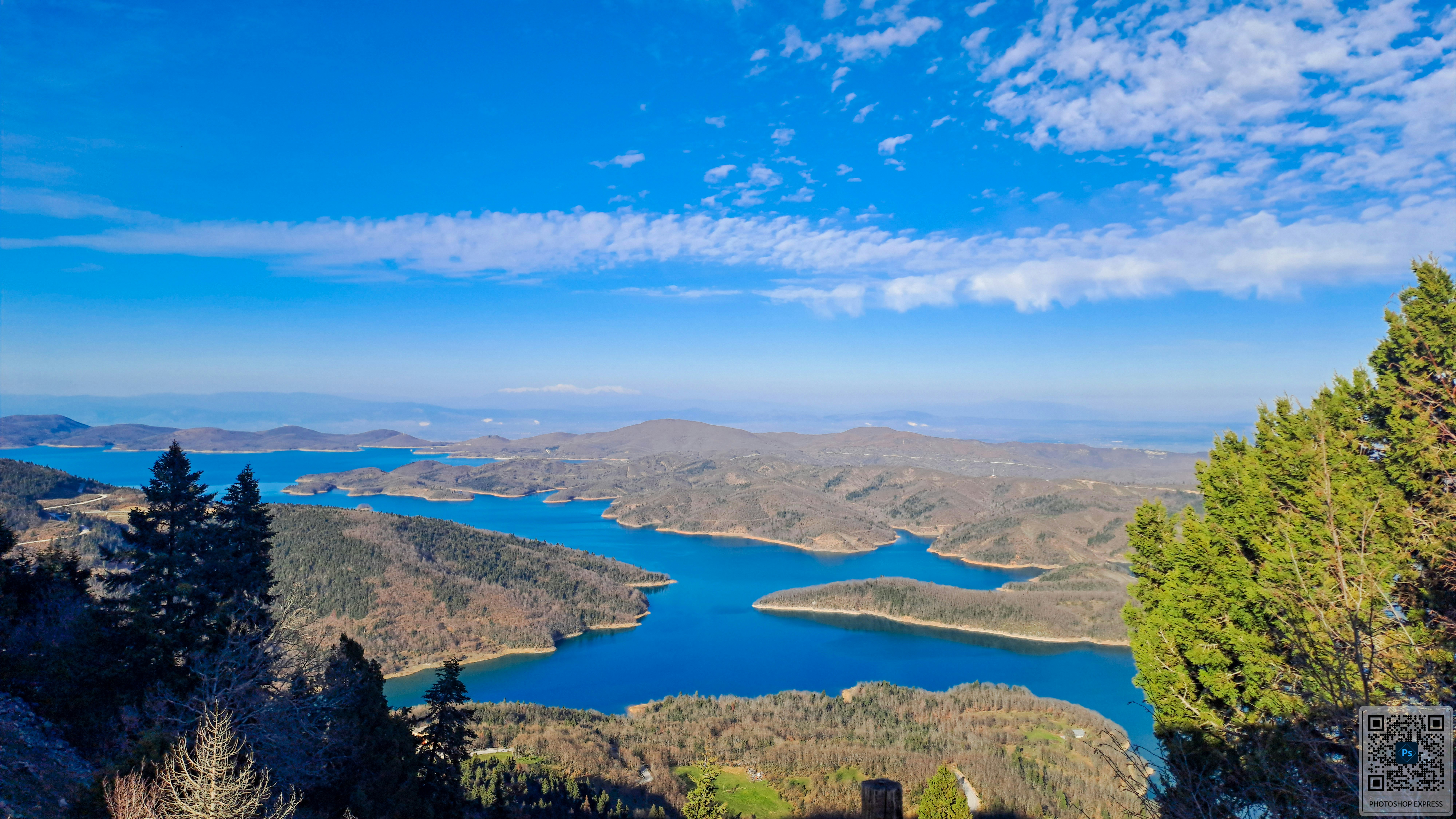 Watchtower of the lake | Vast blue lake winding through forested hills under sky.