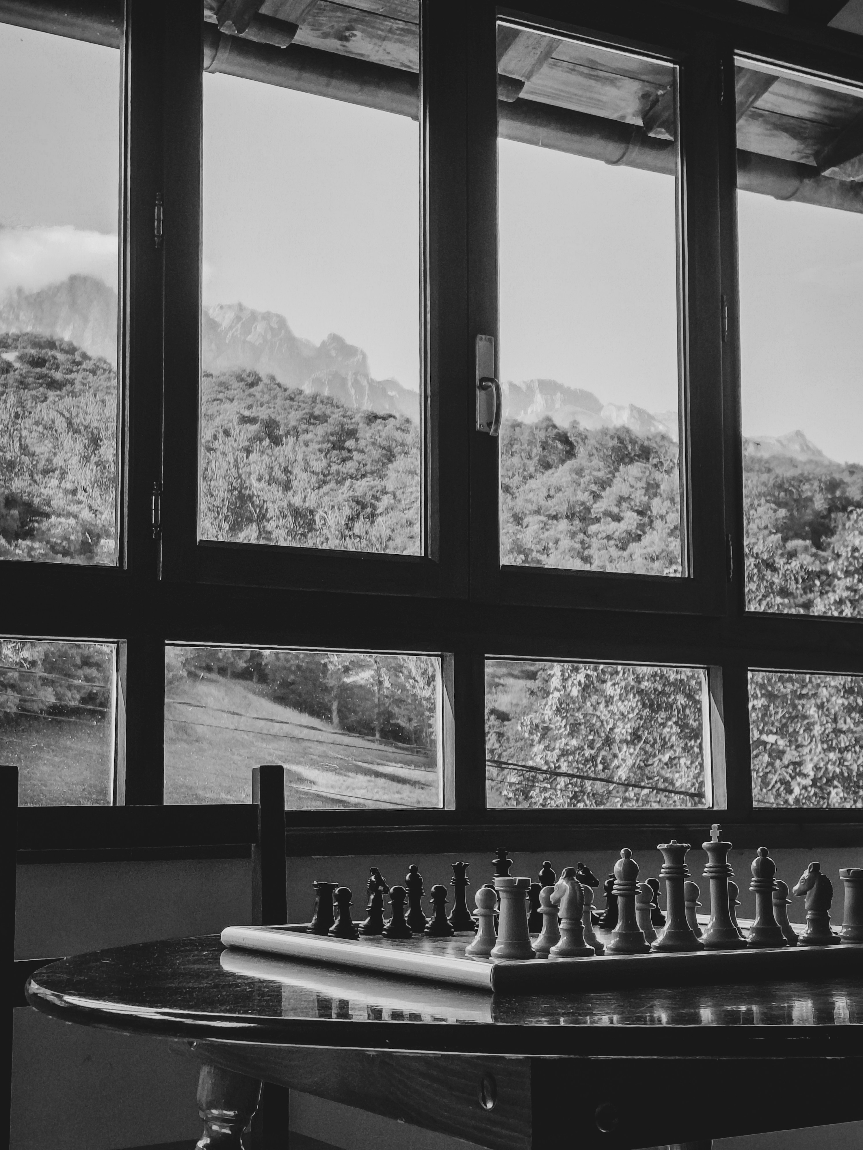 Chessboard set against a backdrop of mountains visible through large windows, creating a serene atmosphere for strategic contemplation.