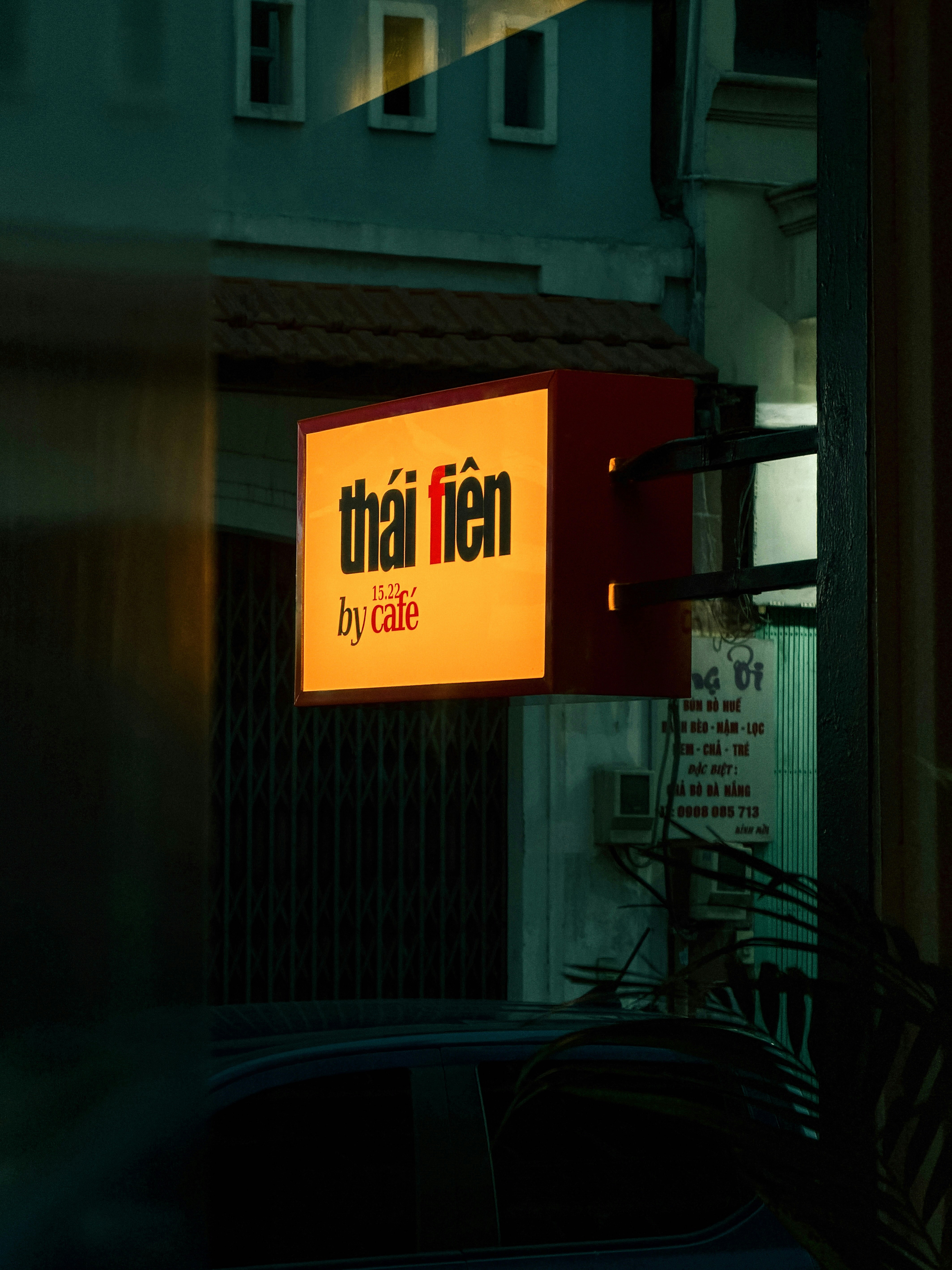Lighting | Illuminated sign for "thai fien by cafe" at dusk.