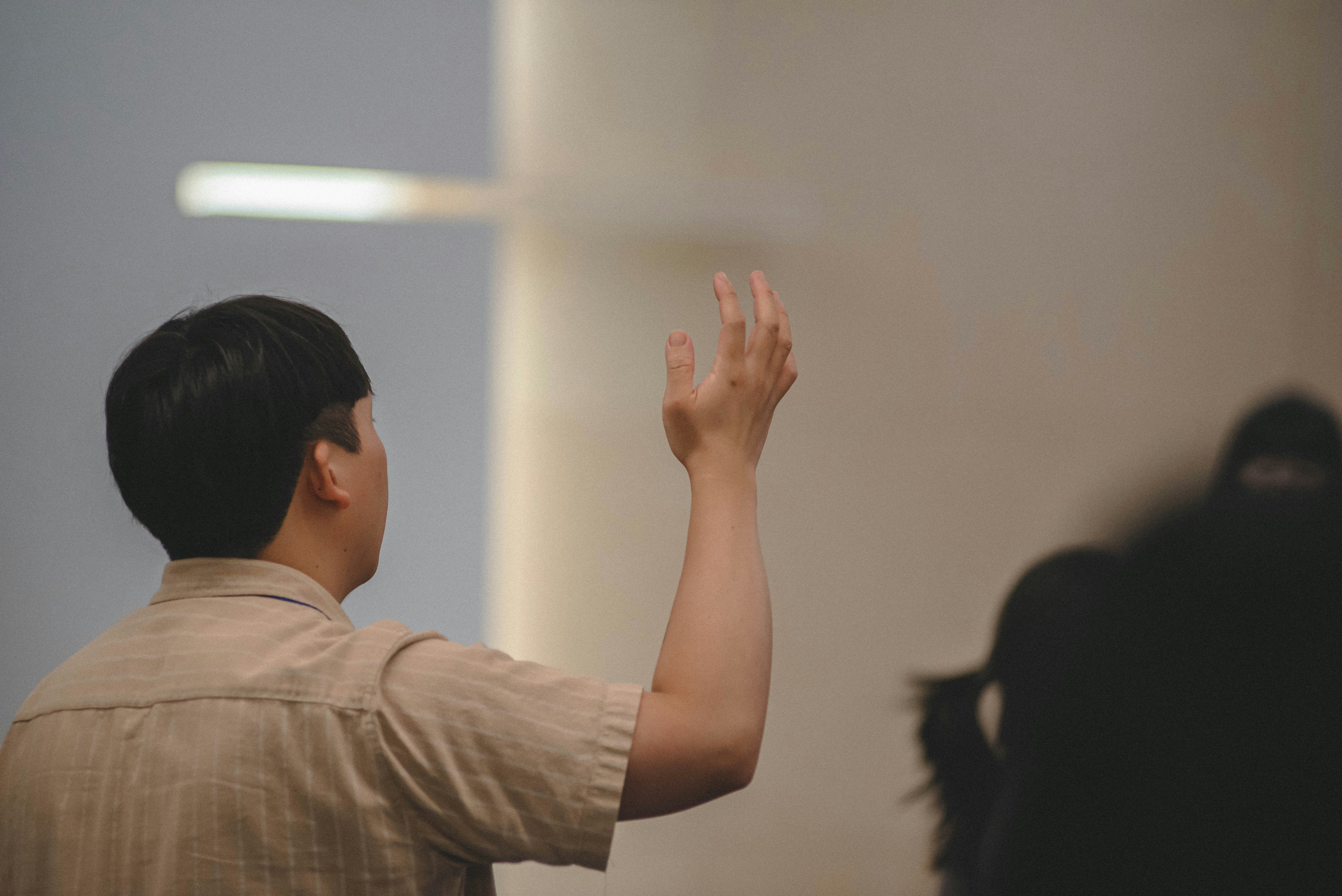 Individual raising hand in a discussion setting, surrounded by blurred figures, highlighting participation and interaction.