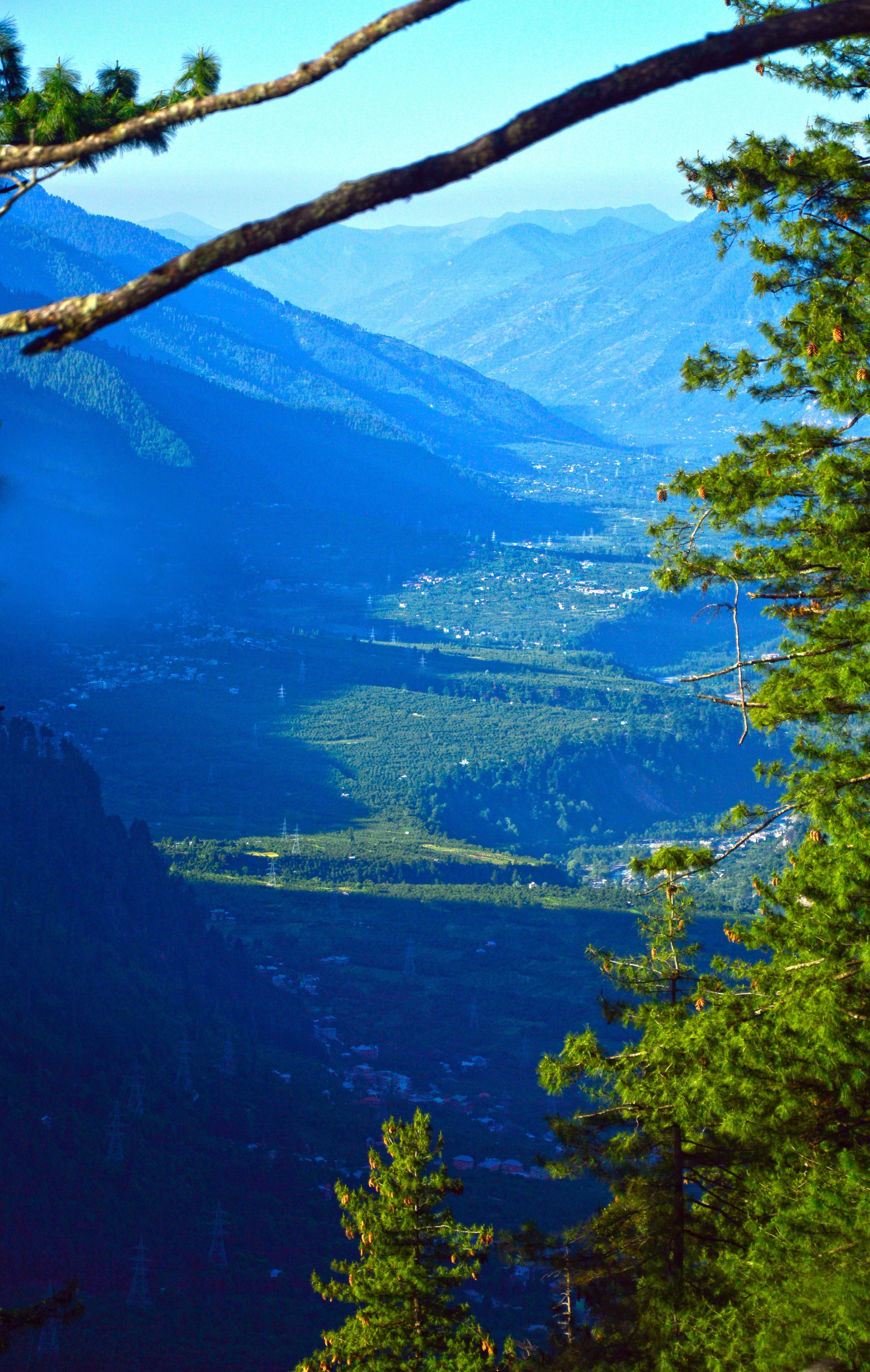 Vast valley framed by towering mountains and lush greenery, showcasing a serene landscape under a clear blue sky.