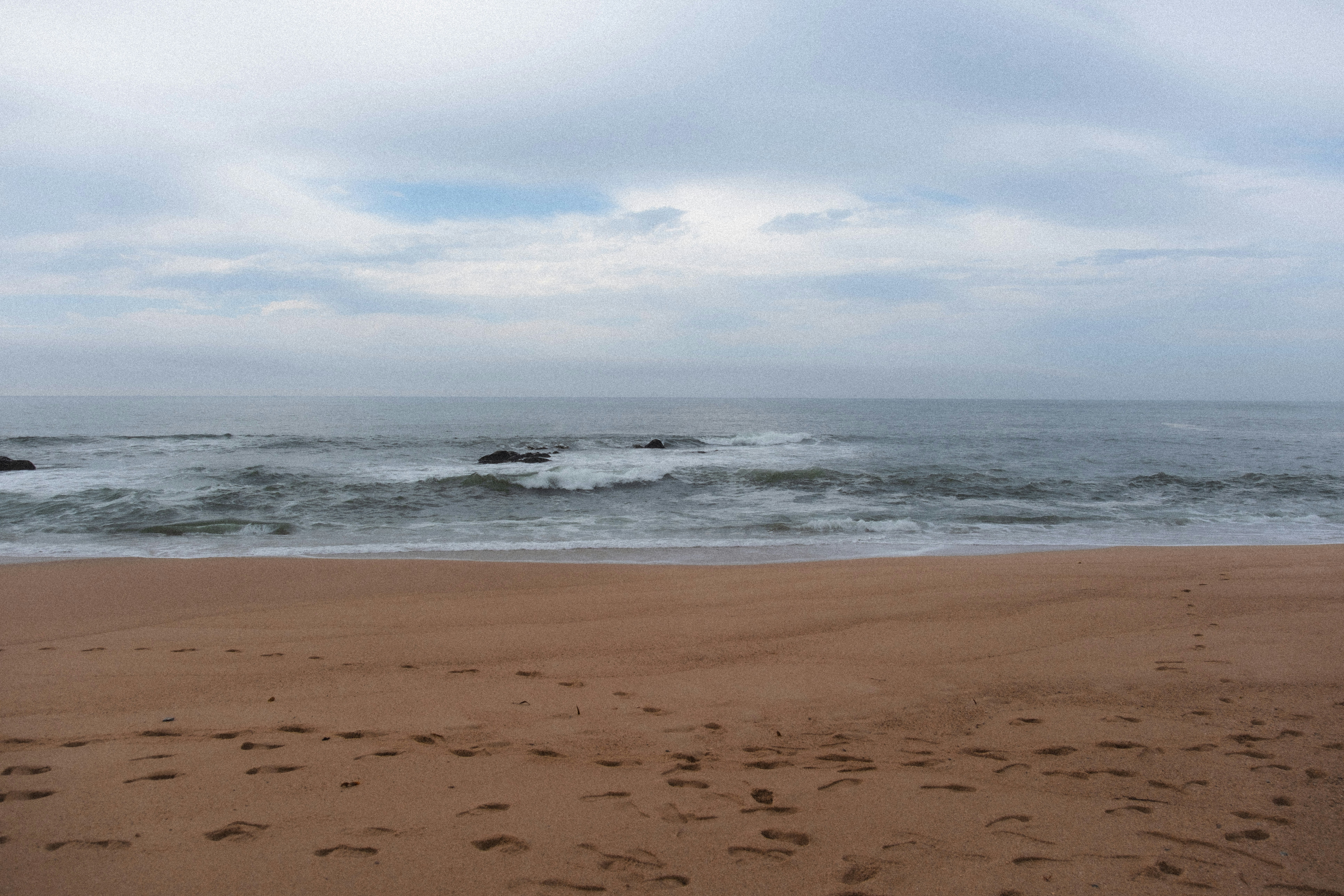 Sandy beach with waves crashing under cloudy sky