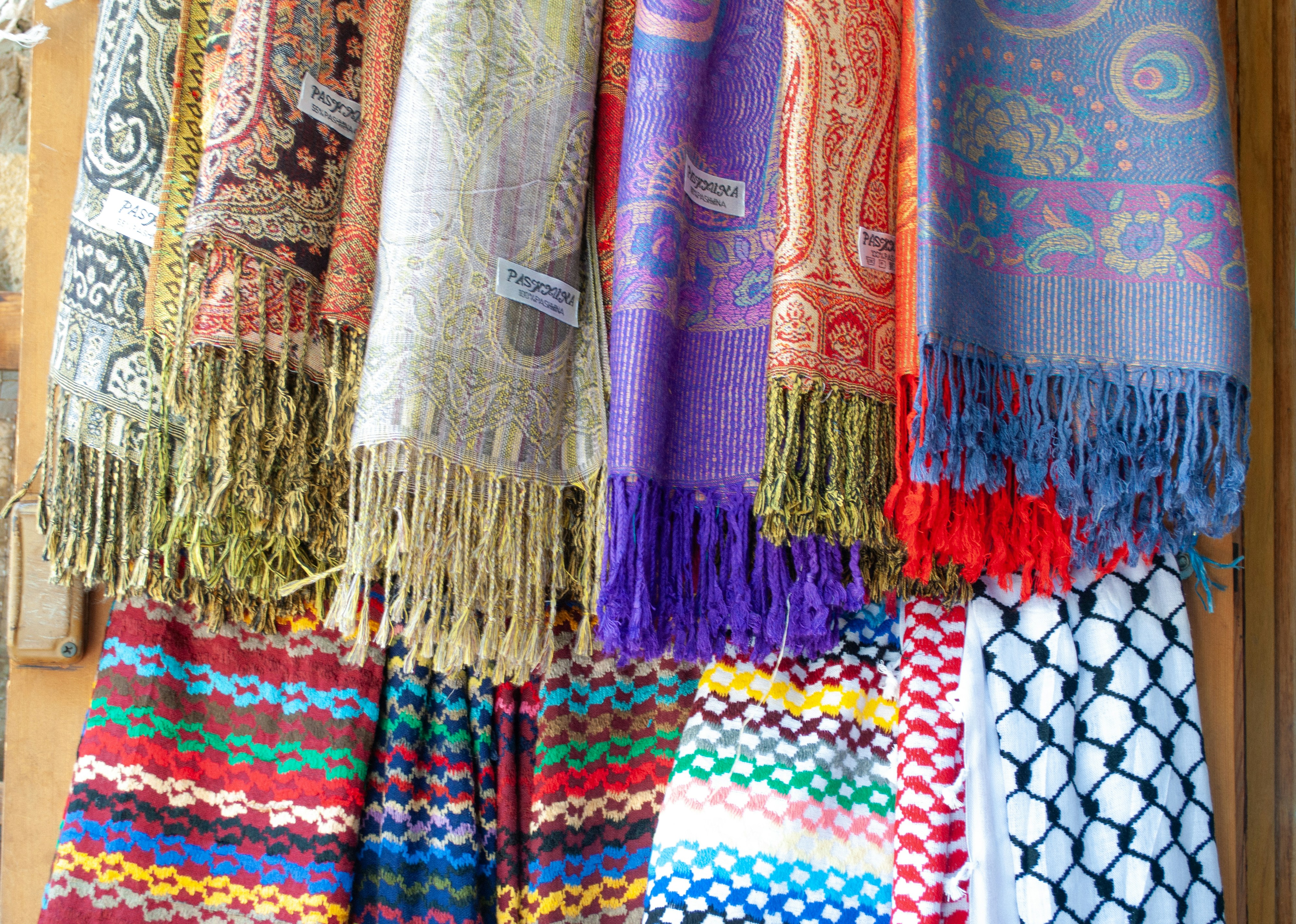 In the old Souq a broad arrays of colors and textures are on display. | Colorful scarves and textiles displayed for sale.