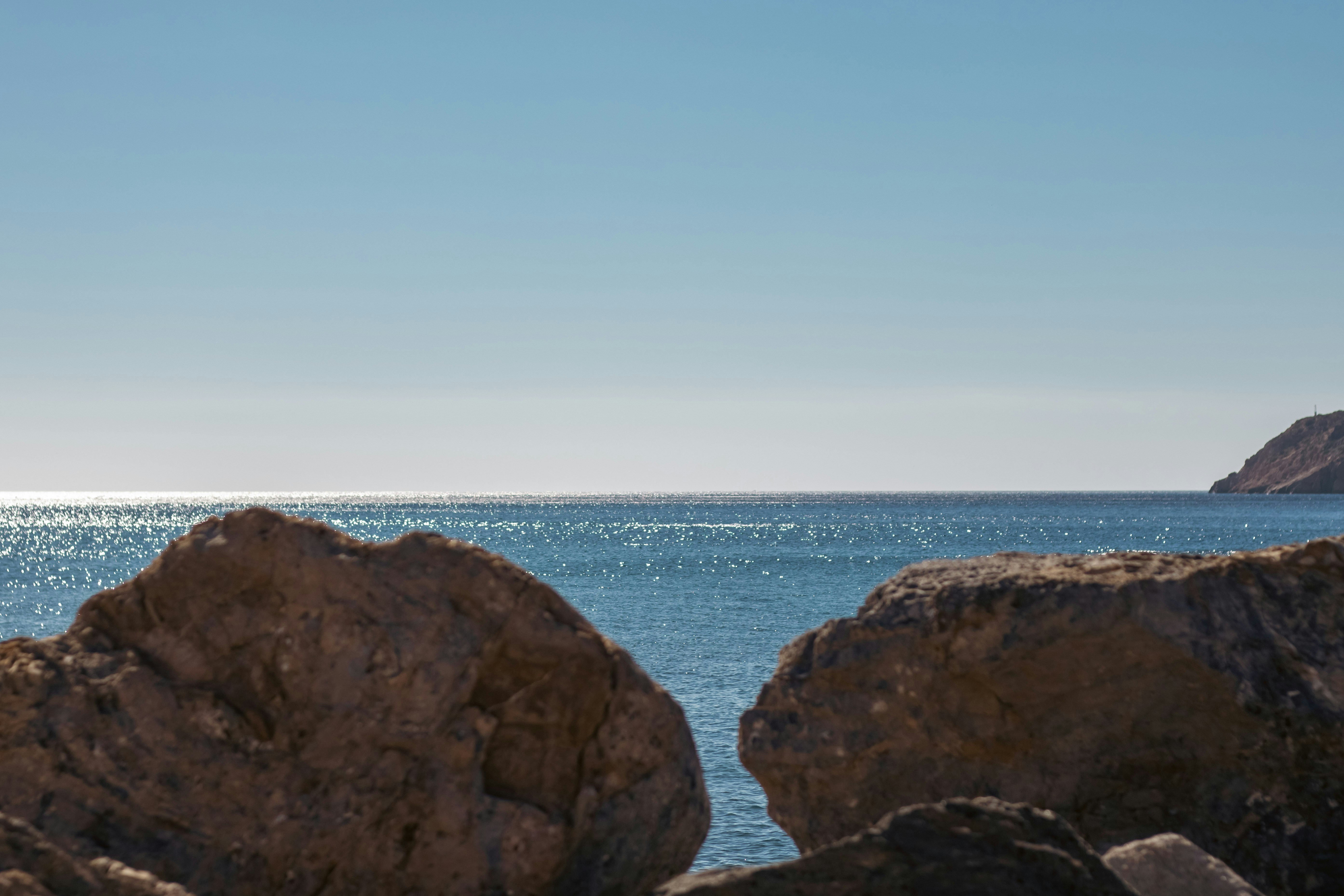 Rocky shore meets the sparkling blue ocean under clear sky