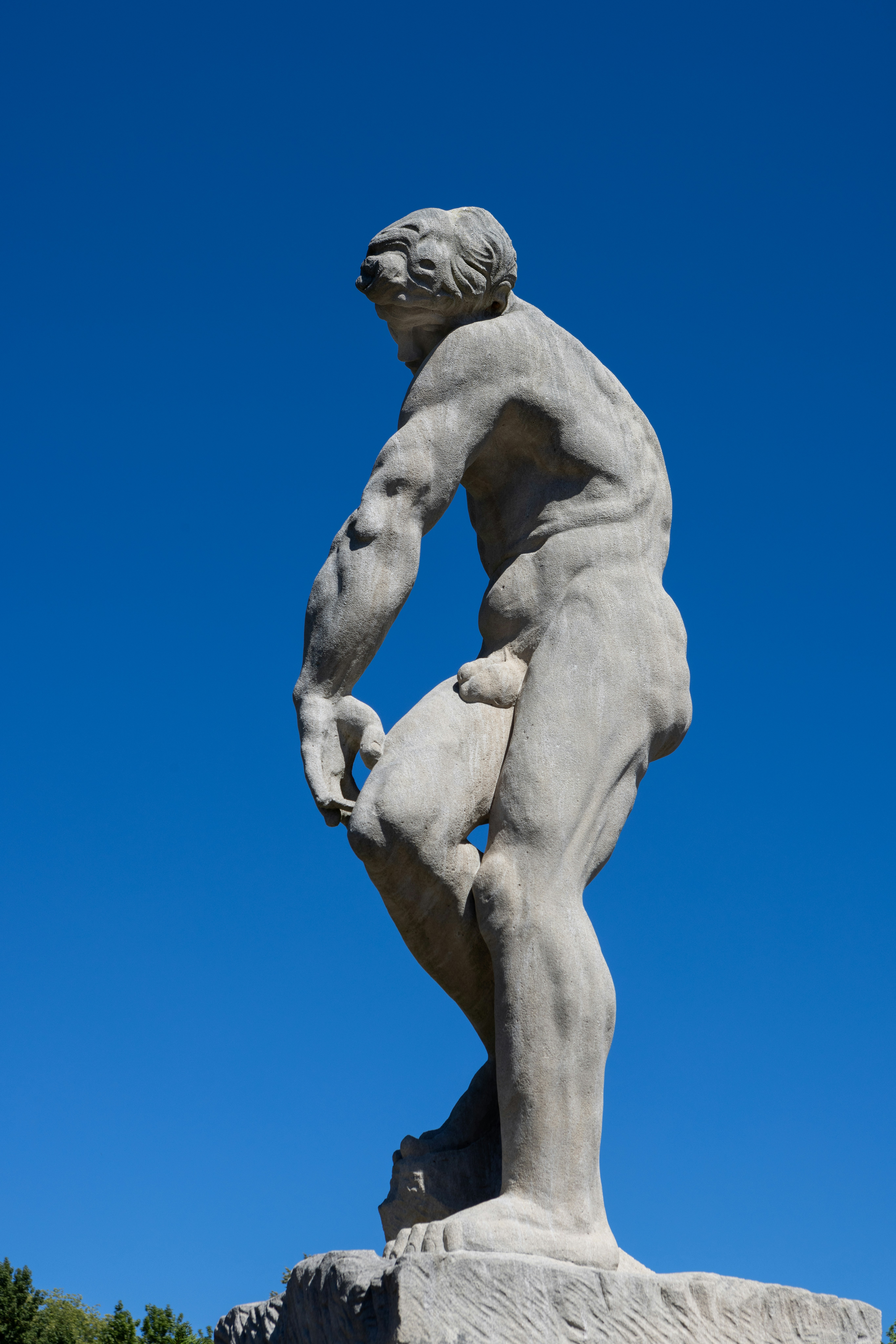 Stone statue of a muscular man against blue sky