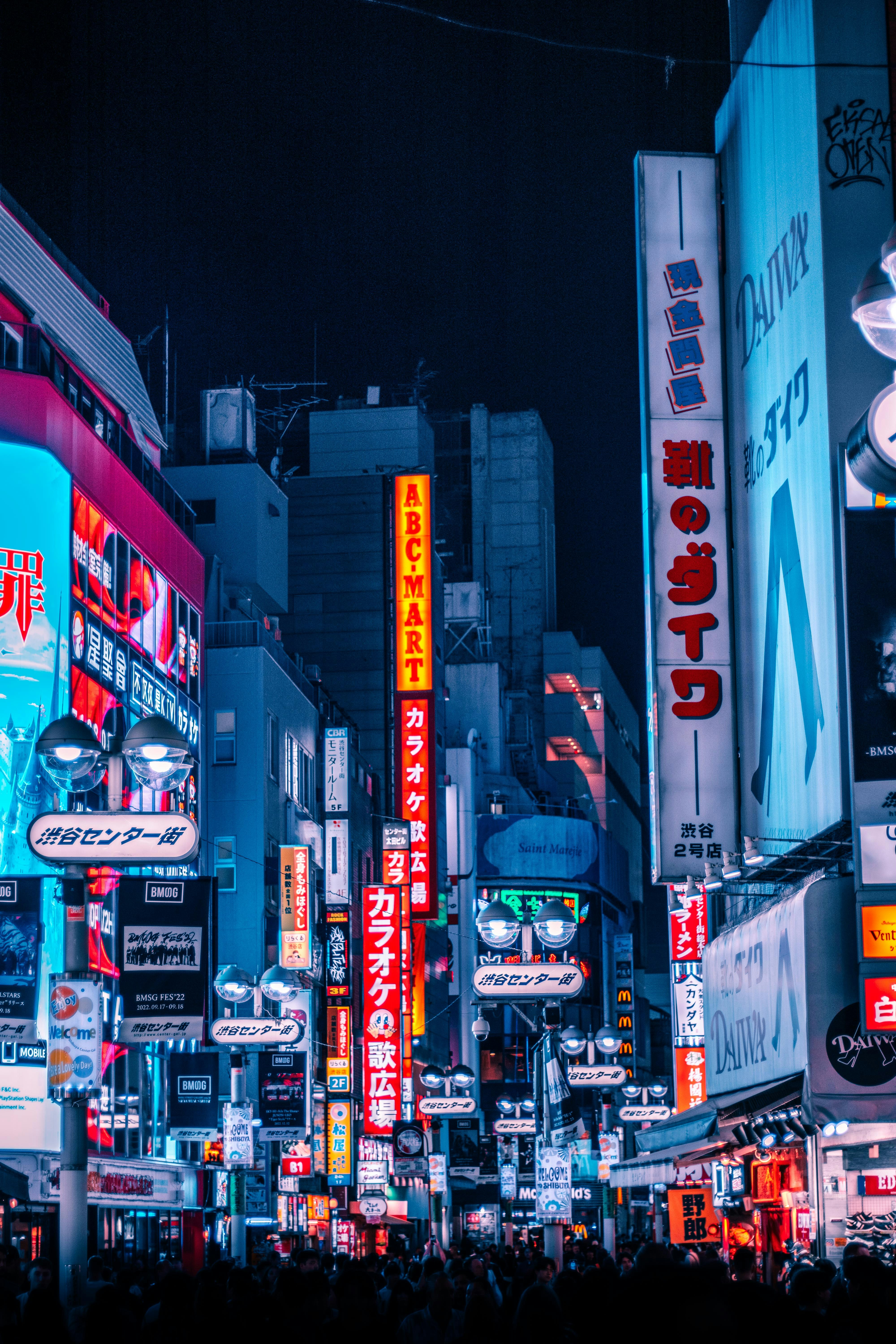 Vibrant cityscape illuminated by colorful neon signs, showcasing the lively atmosphere of urban nightlife. A mix of modern architecture and bustling crowds creates a dynamic scene.