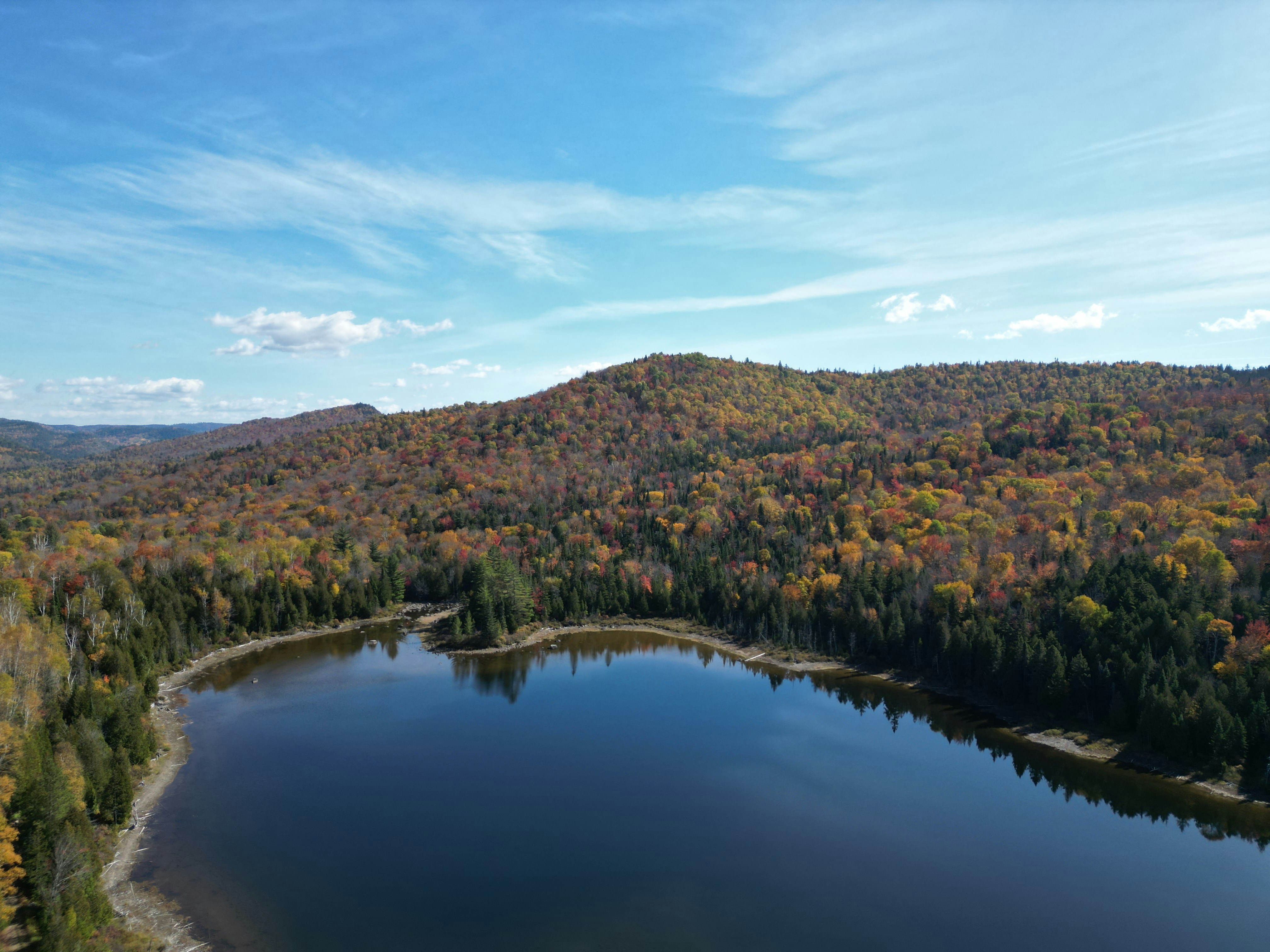 Vibrant autumn foliage reflects on a serene lake surrounded by rolling hills. The scene captures the essence of fall's beauty.