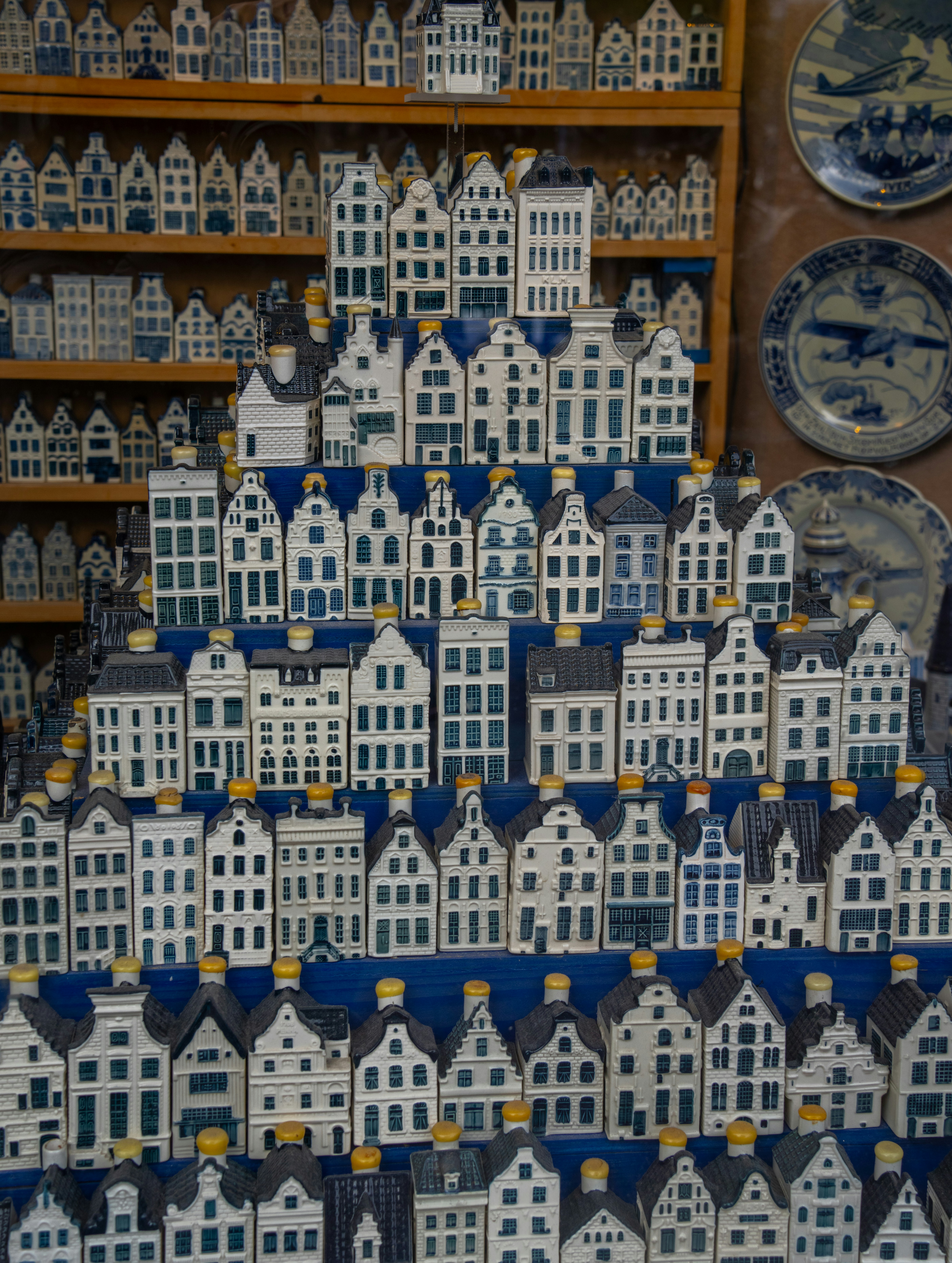 A meticulously arranged display of ceramic houses, showcasing intricate architectural details and vibrant colors. The backdrop features decorative plates enhancing the cultural theme.