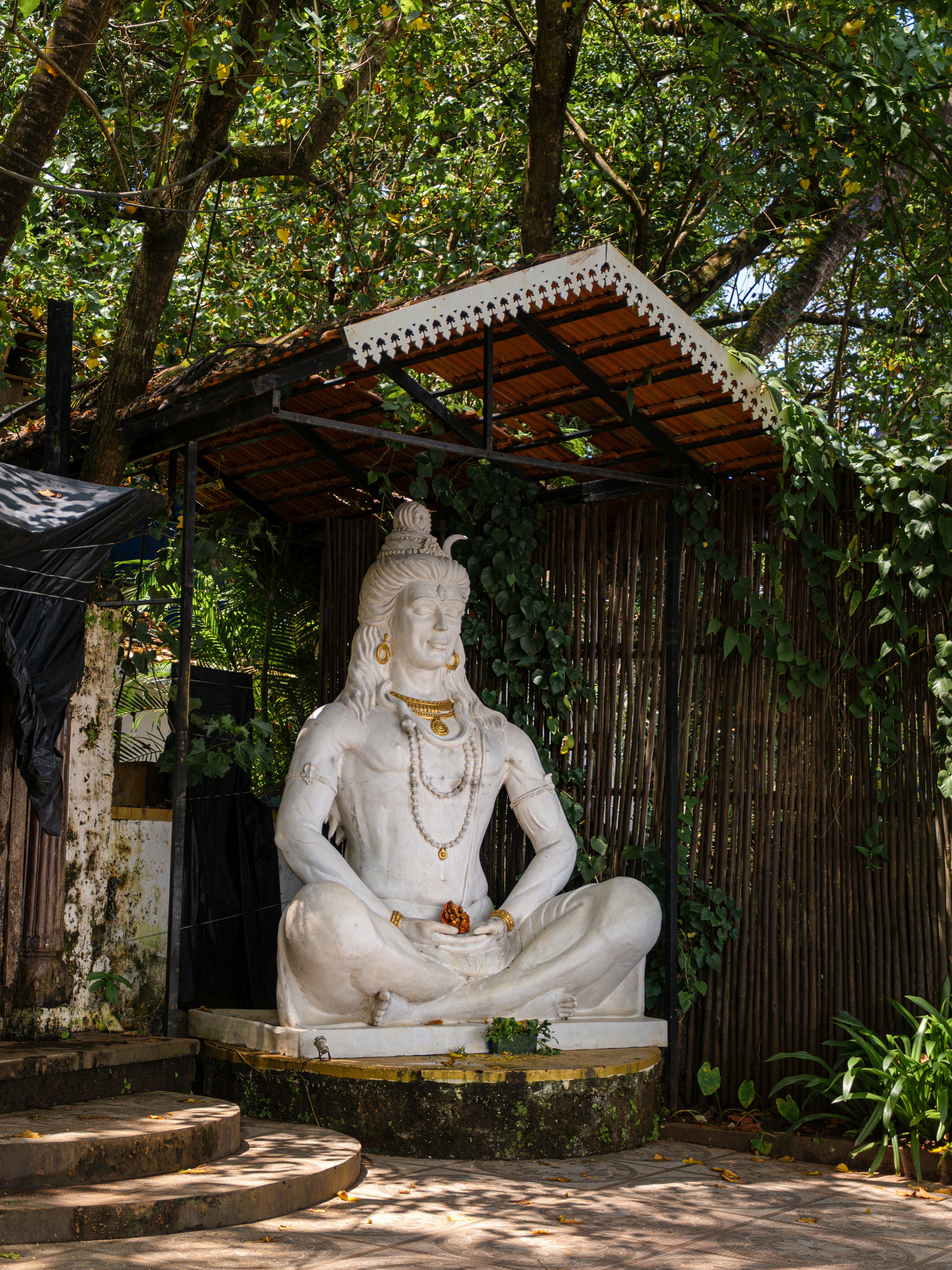 White Hindu Deity Statue Resting Under a Leafy Canopy