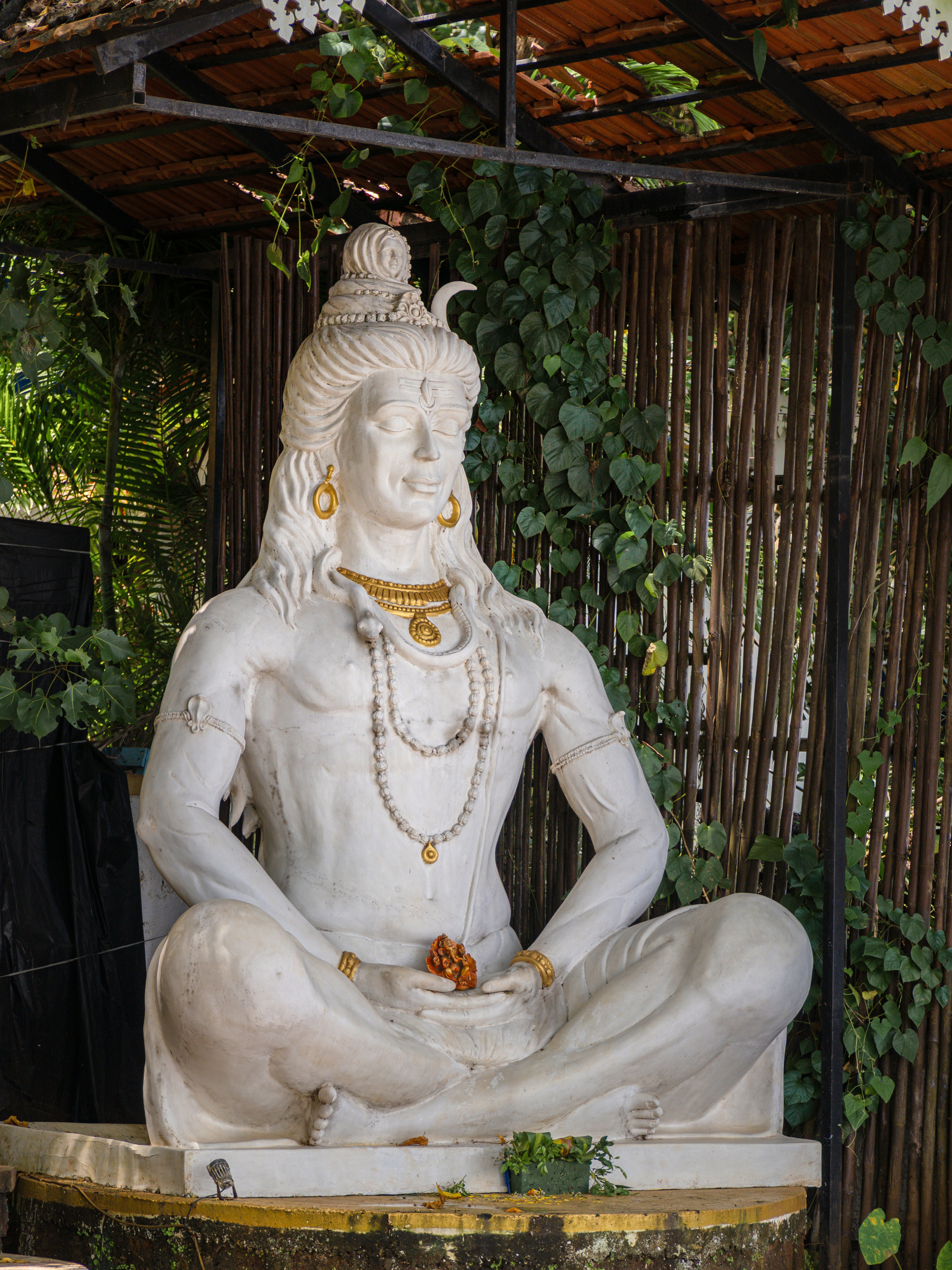 Shiva in Serenity: A White Marble Meditating Statue Beneath a Verdant Shelter