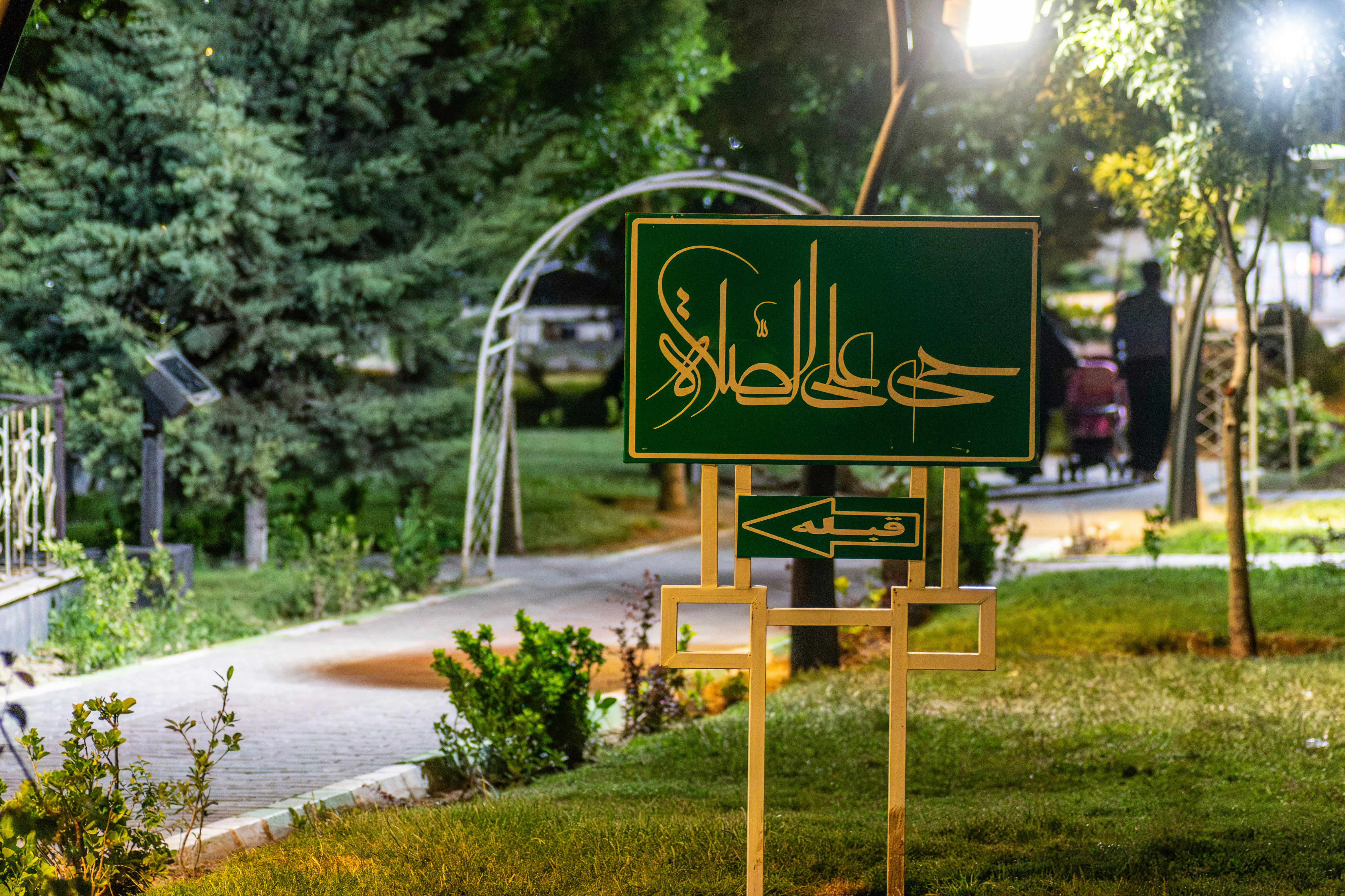 Green sign with arabic calligraphy and directional arrows