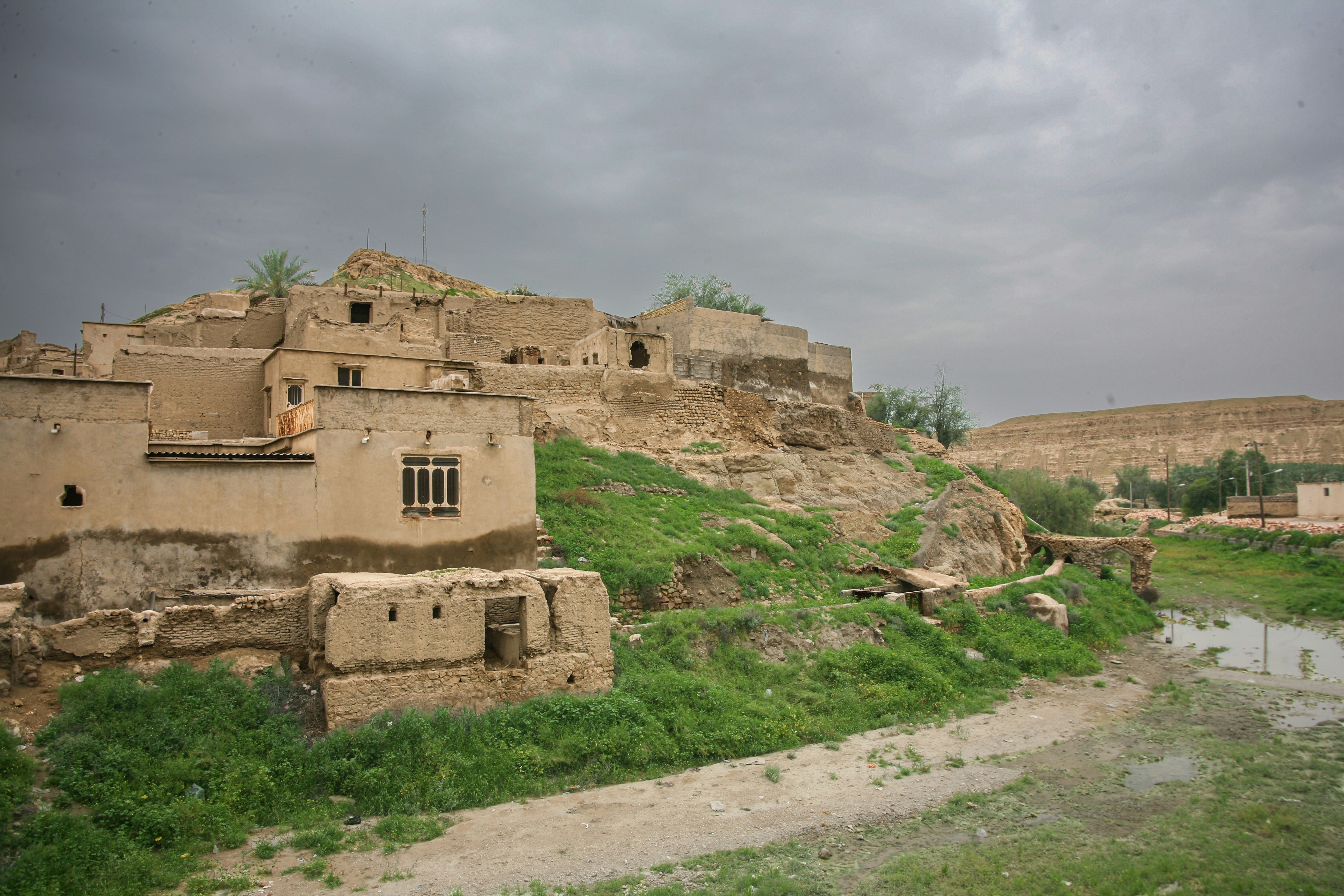 Ancient village ruins on a grassy hillside under cloudy skies.