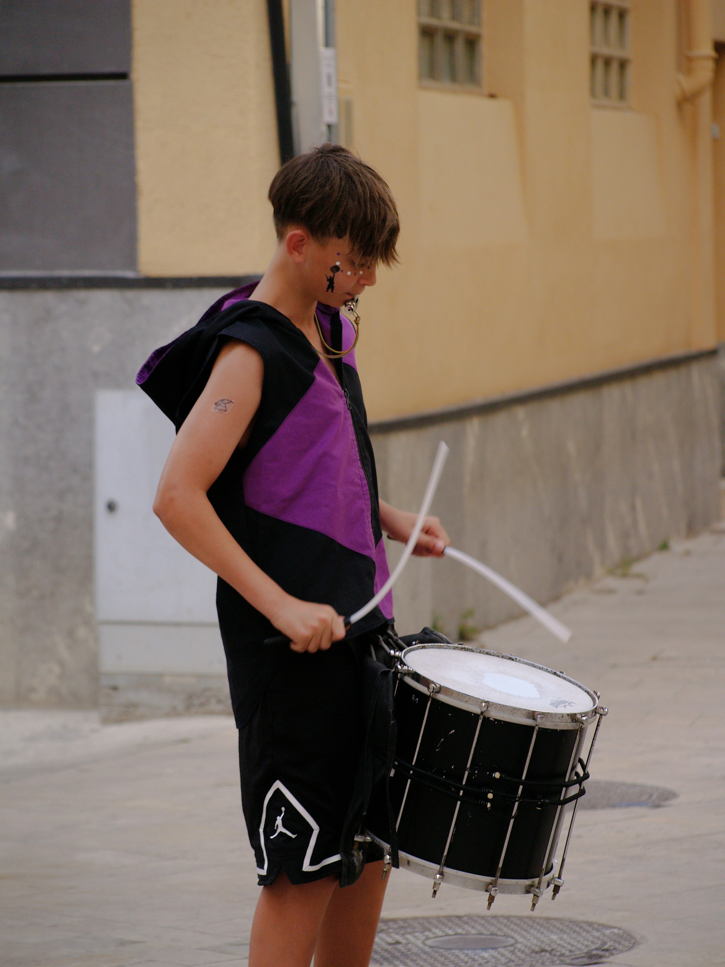 OLYMPUS DIGITAL CAMERA | Teenager playing a drum with sticks outdoors.