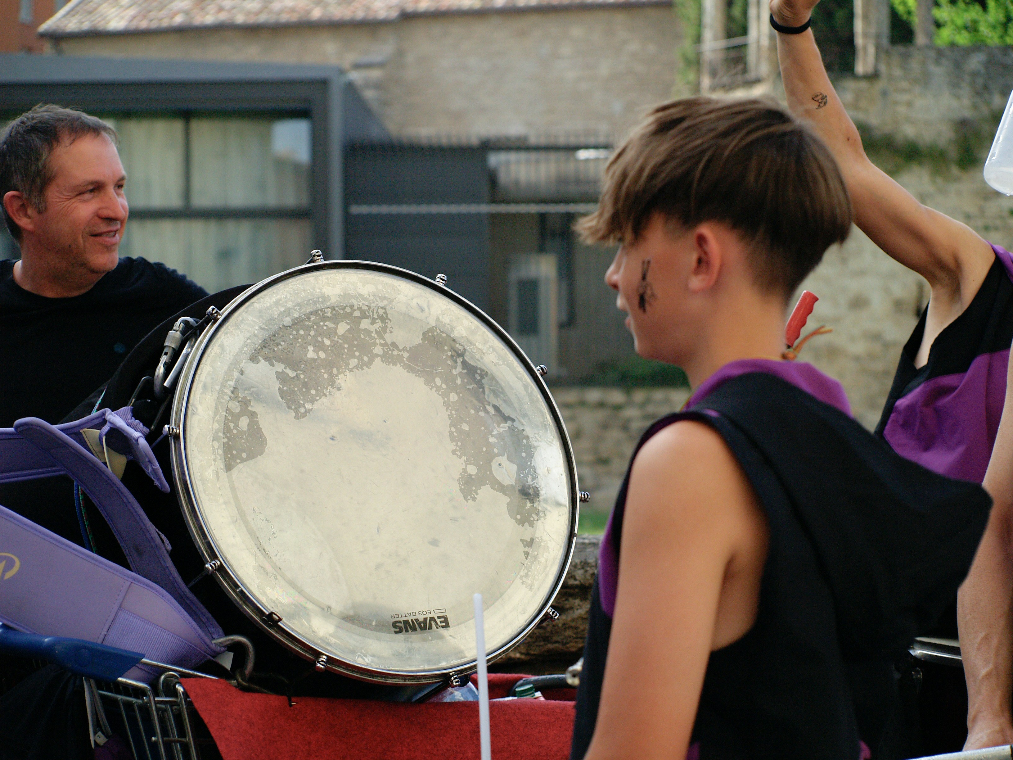 OLYMPUS DIGITAL CAMERA | Young person playing a large drum with a man watching