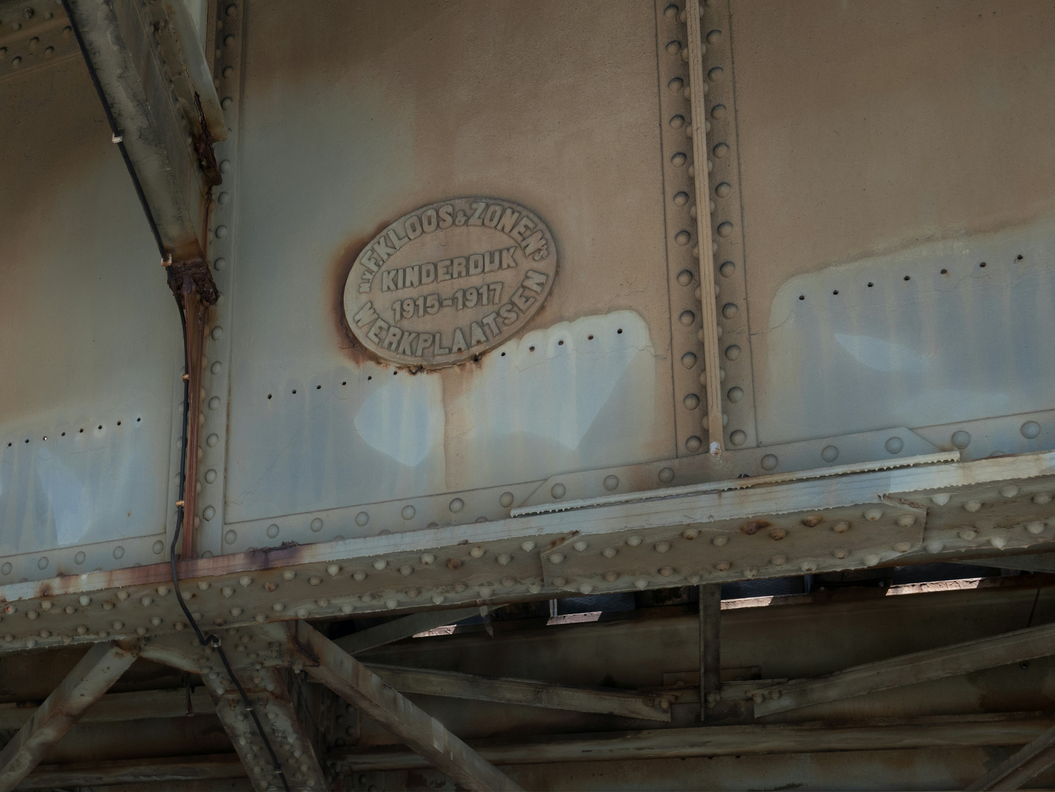 Close up of the logo / icon of the compagny who built this old cast irontrain bridges in 1915 - 1917 over the canal Oostertoegang at the east side of Central Station in Amsterdam city. They are now demolished and replaced by new bridges. Free image of The Netherlands. | Close up of a metal plaque on a bridge
