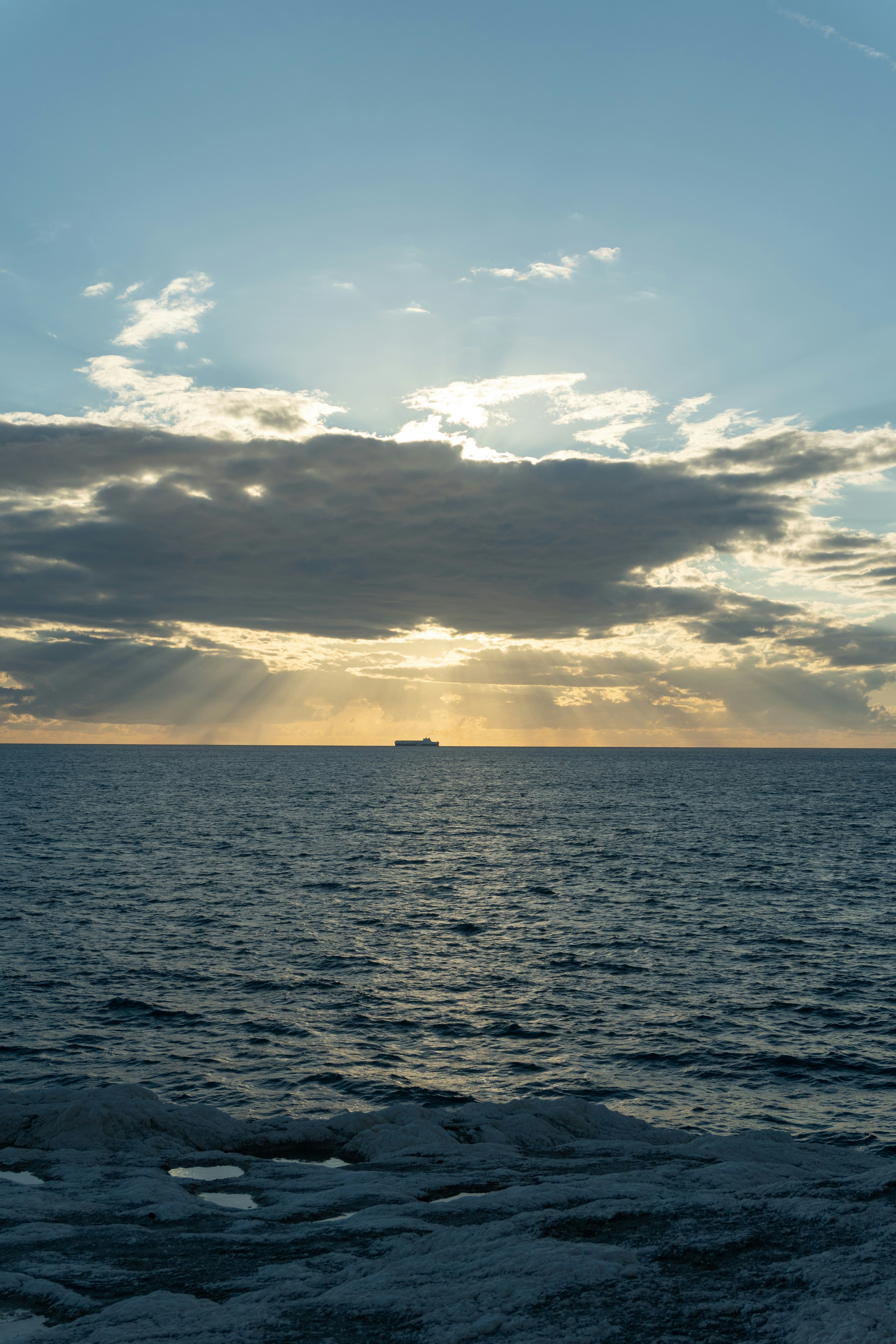 Ship on the ocean at sunset with sunbeams.