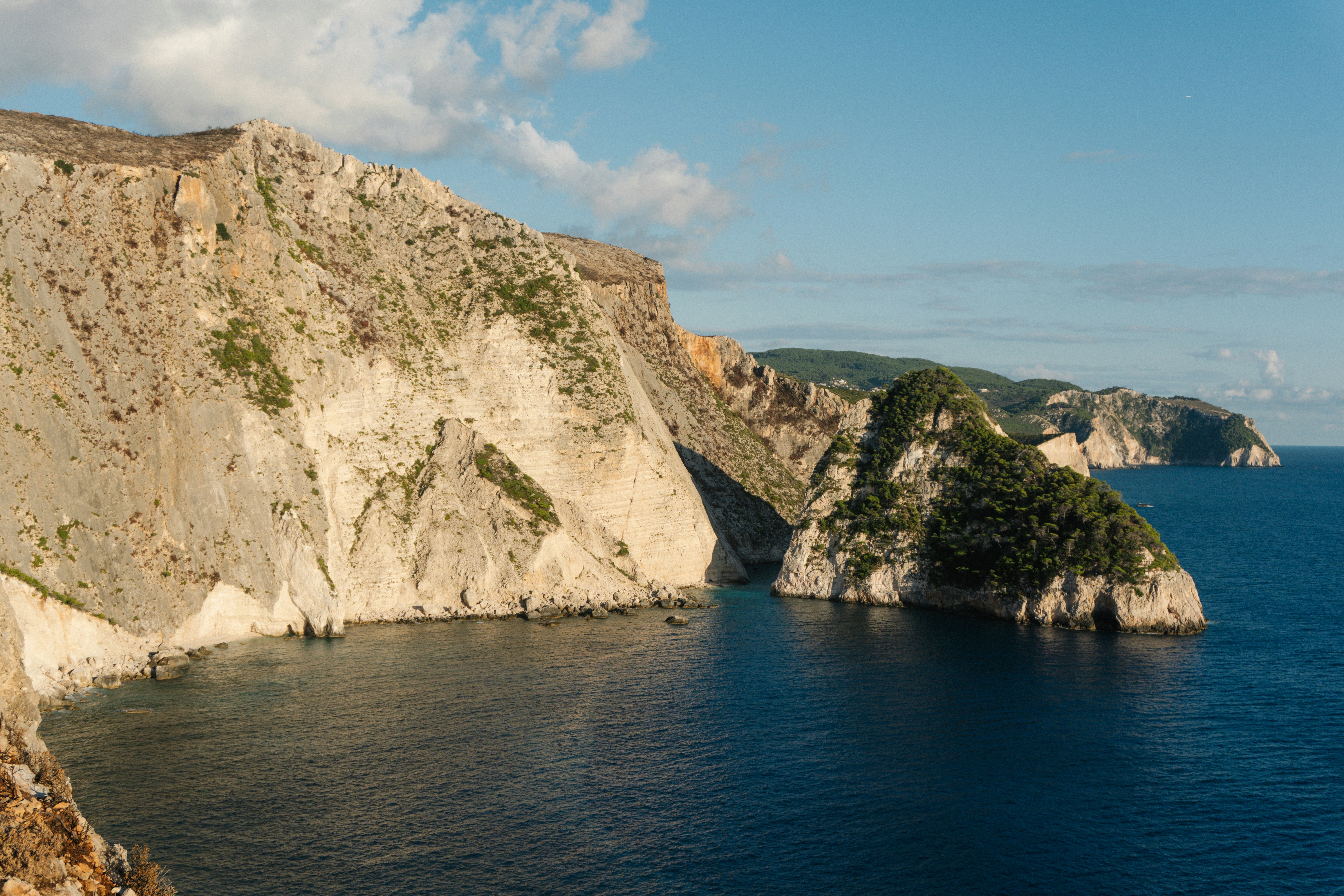 Rocky cliffs meet the deep blue sea under a sky.
