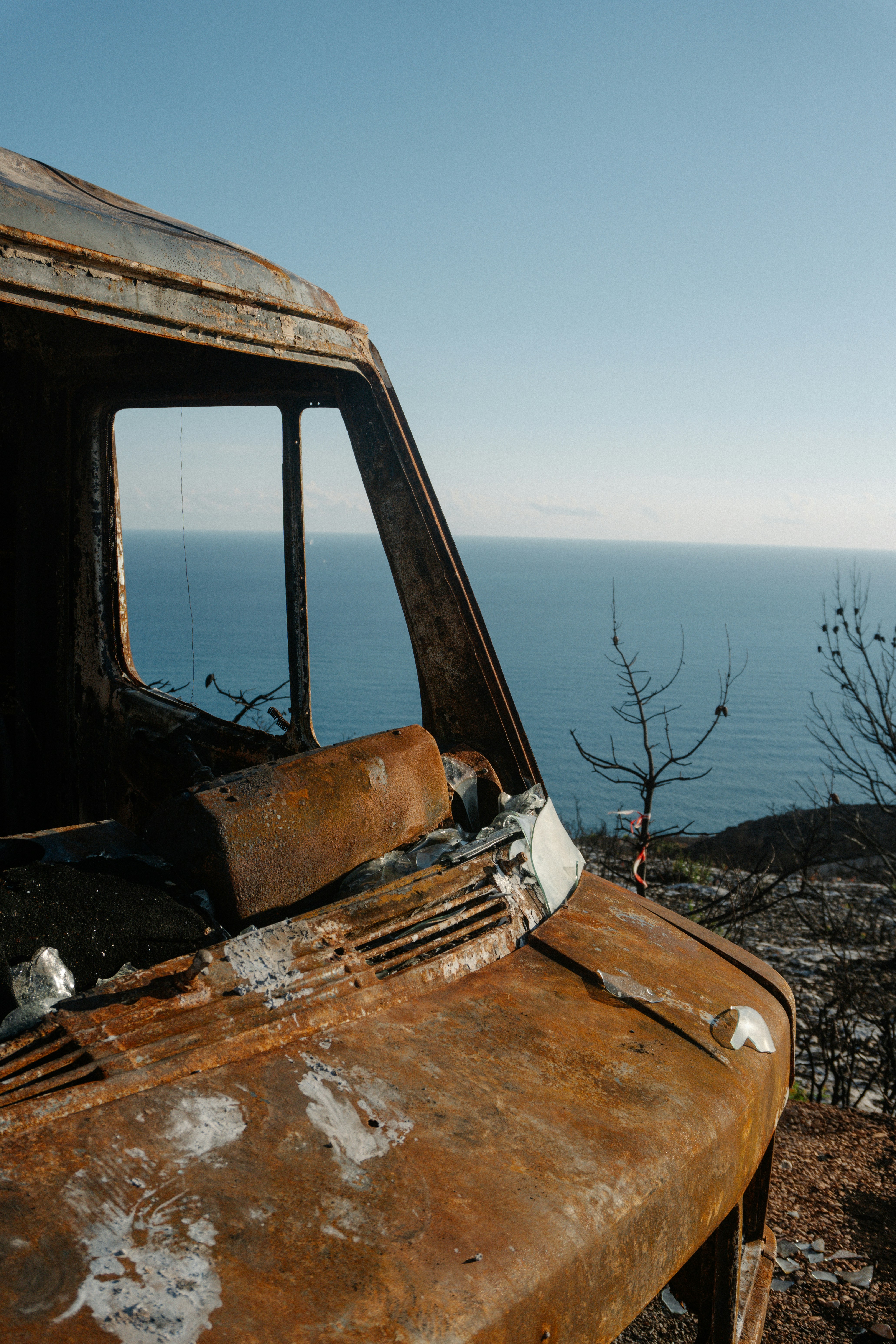 Rusty vehicle remnants overlook a serene ocean view, capturing the contrast between decay and nature's beauty.