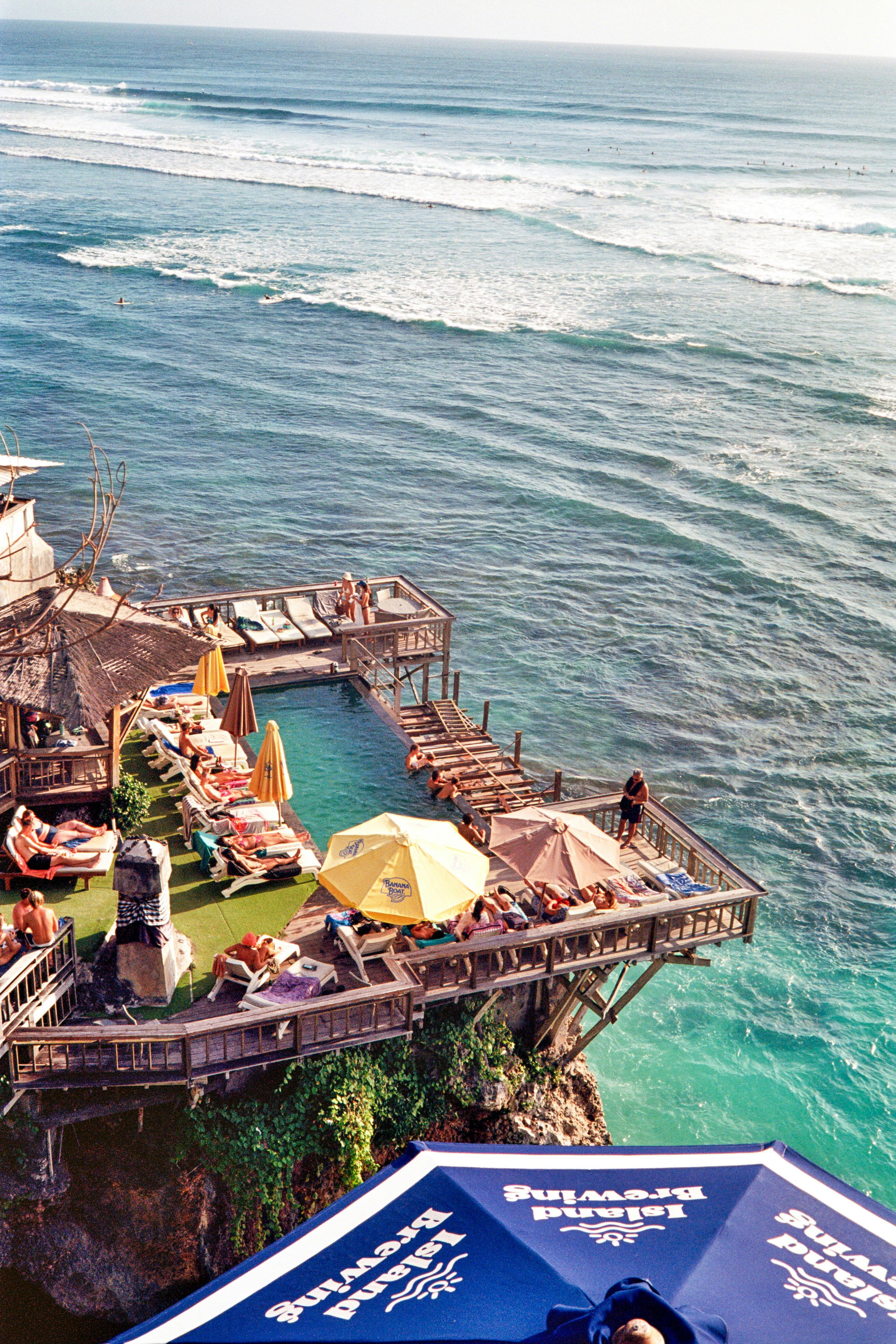 A vibrant seaside deck featuring loungers and umbrellas, overlooking the ocean waves. The scene captures a relaxing atmosphere with sunbathers enjoying the coastal view.