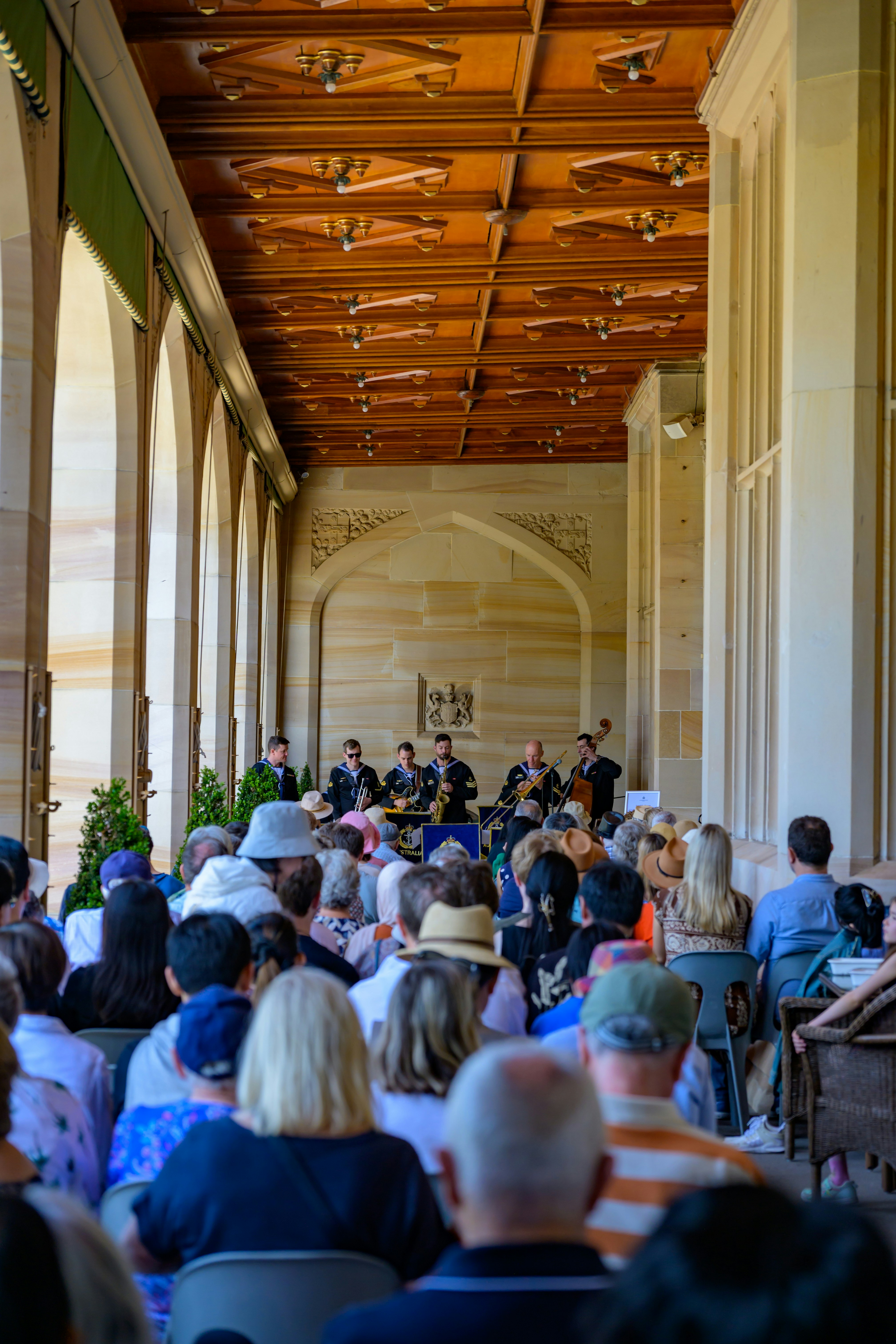 Ensemble performing in a beautifully adorned courtyard, surrounded by an attentive audience. Lush greenery and intricate architecture frame the scene.