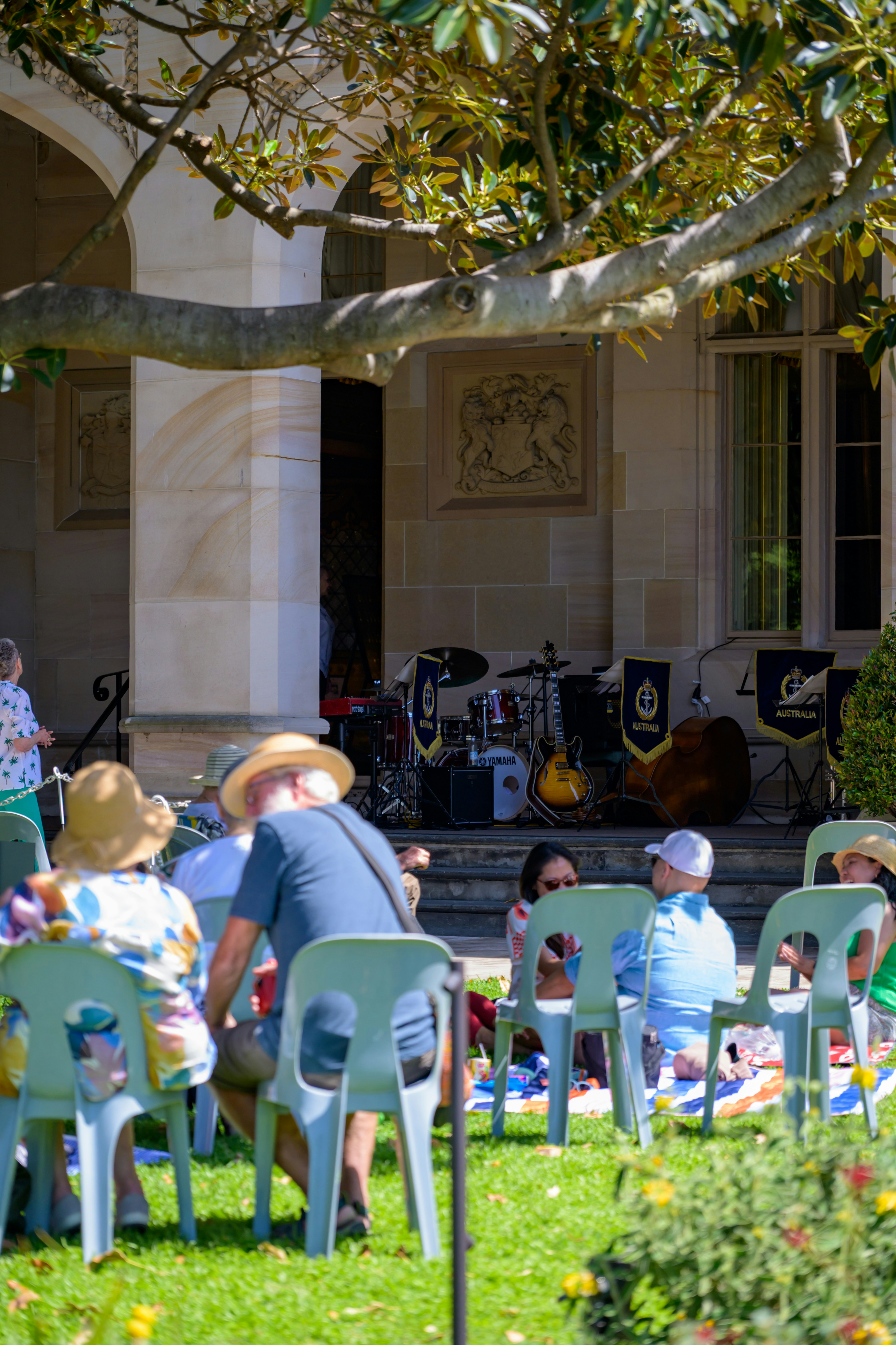 People sit on chairs watching a band perform outdoors.