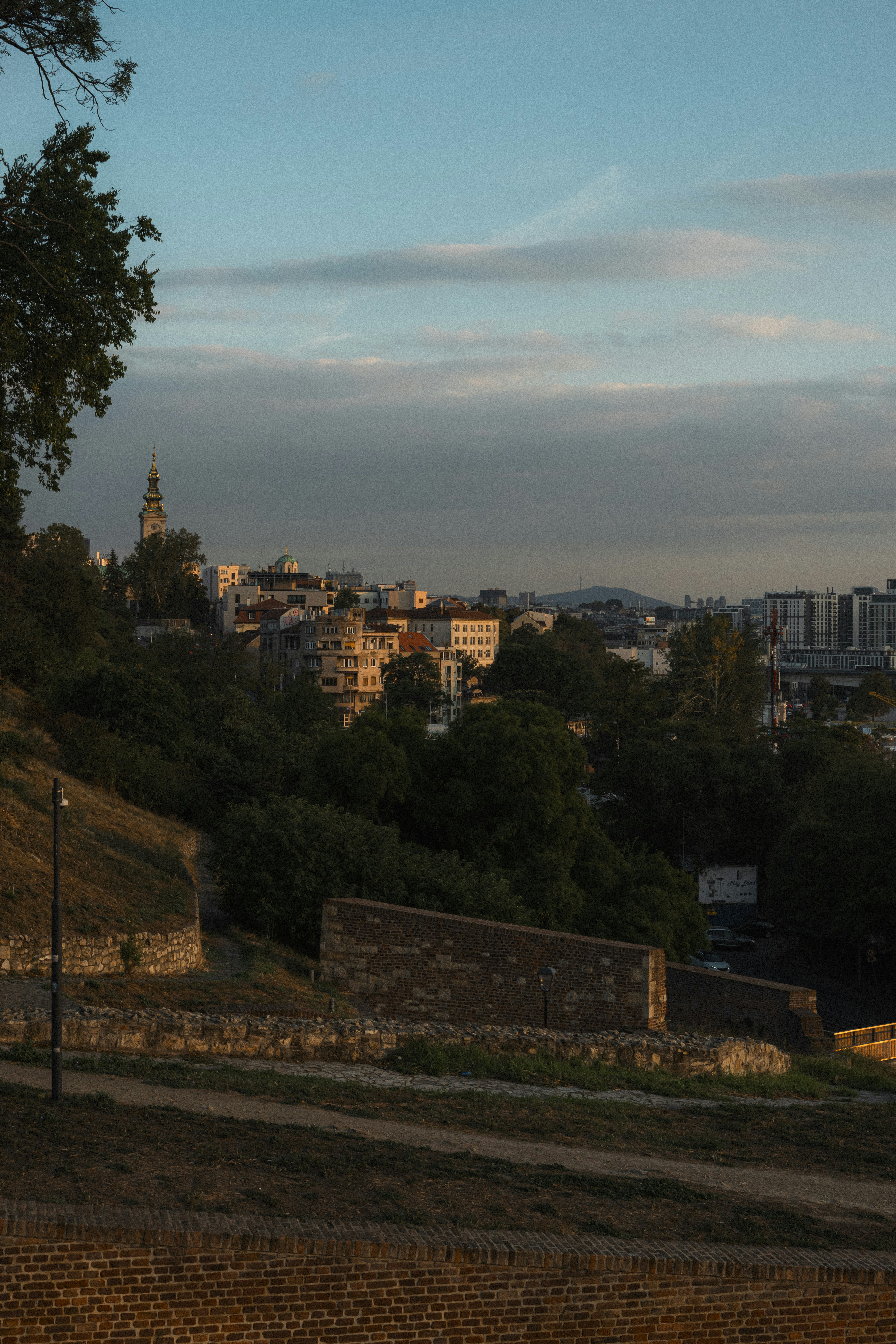 A serene cityscape bathed in the warm glow of dusk, showcasing a blend of historic and modern architecture against a backdrop of lush greenery.