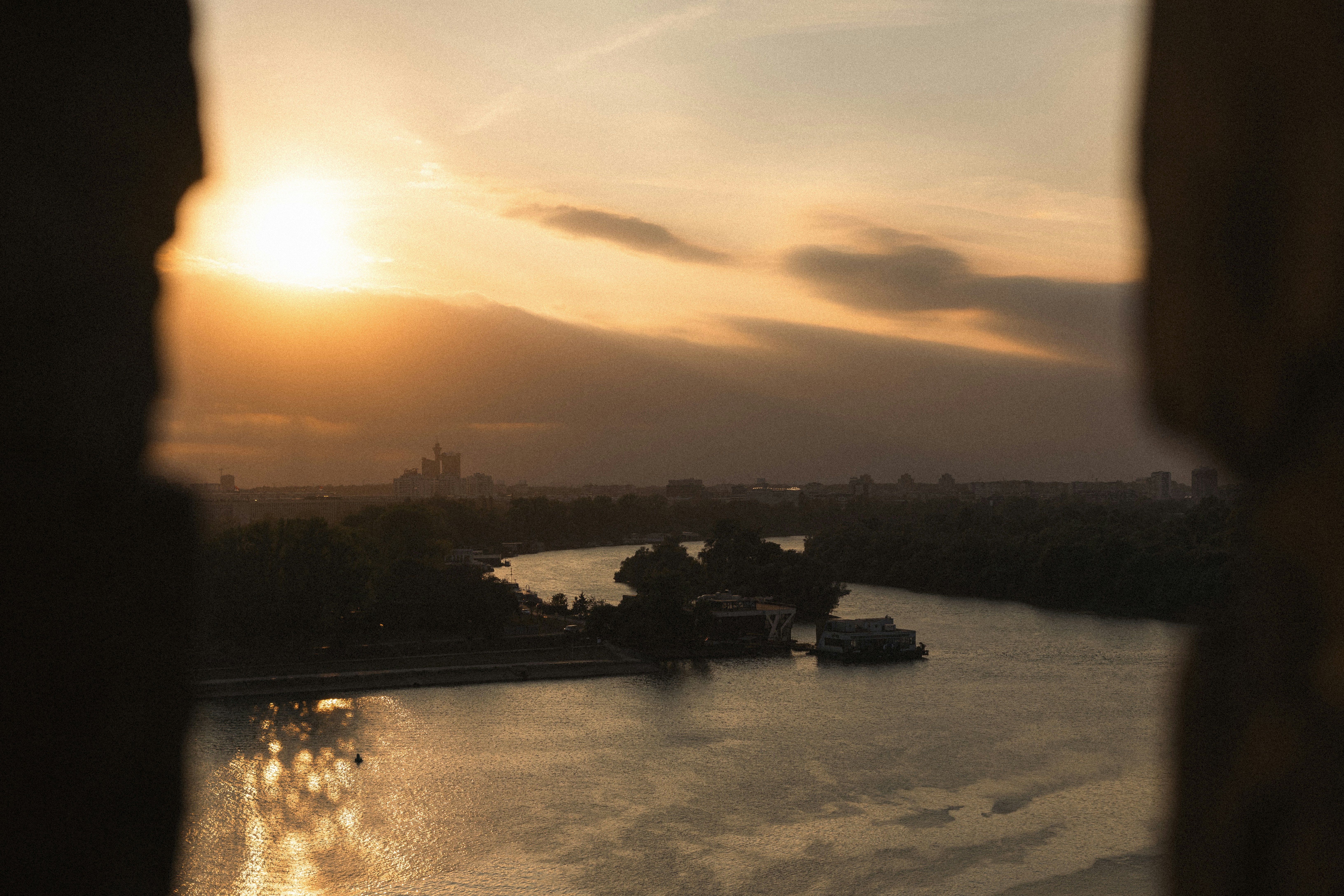 Sunset casting golden hues over a winding river, framed by rocky silhouettes. The scene captures the tranquil beauty of nature meeting urban life.
