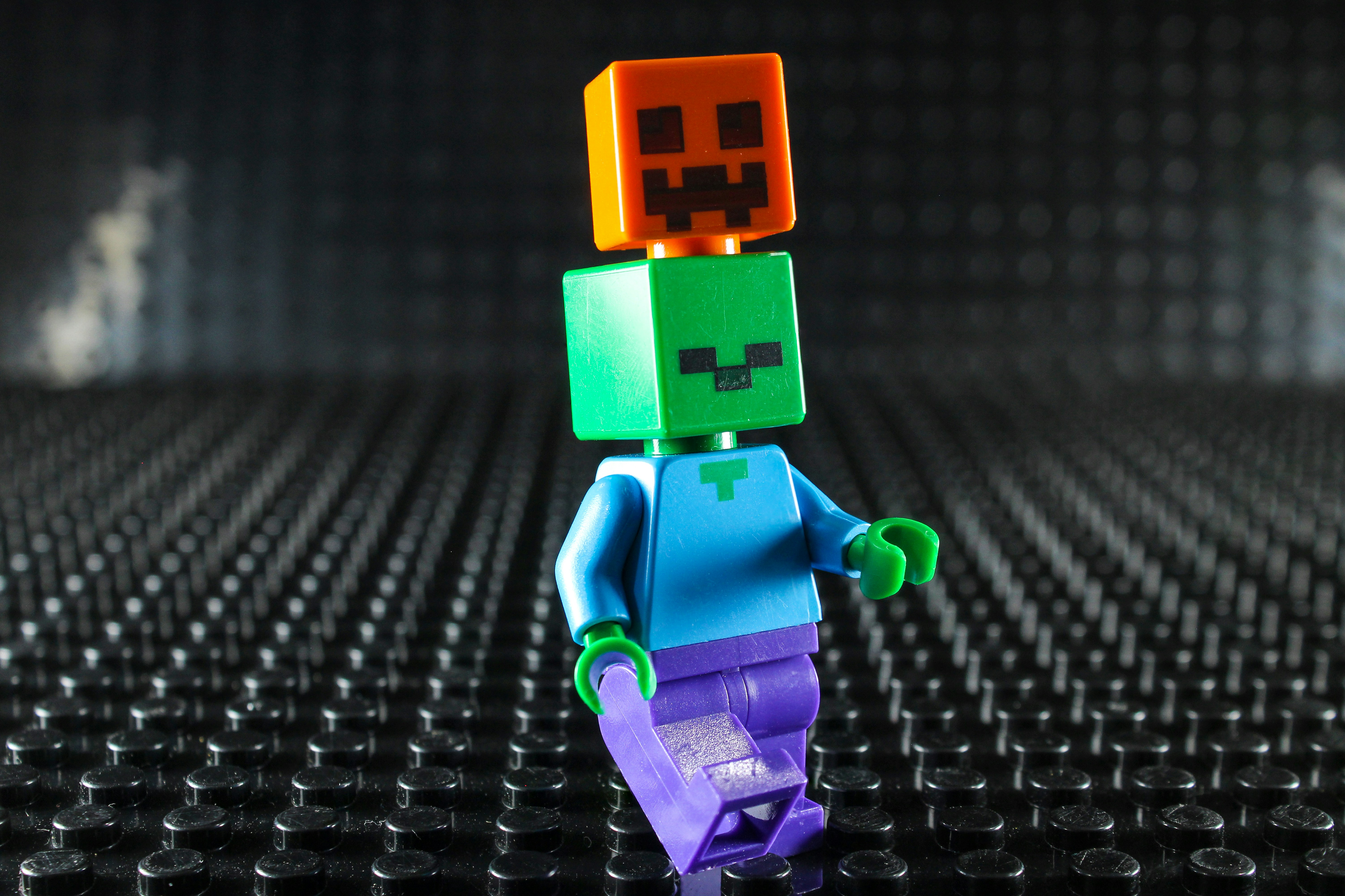 Colorful block figure with a green and orange head stands on a textured black surface, showcasing playful character design.