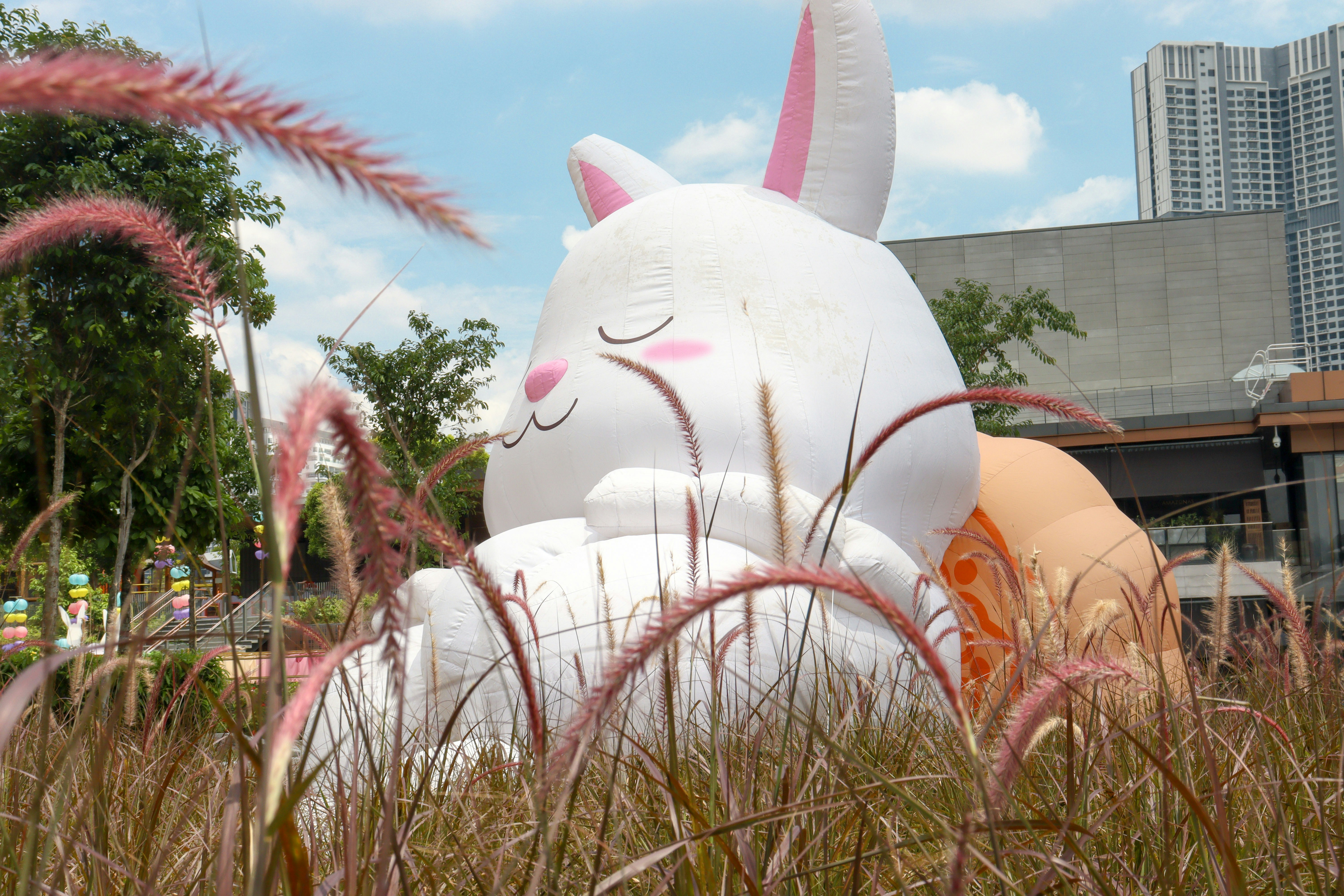 A large inflatable bunny rests peacefully among tall grass, exuding a sense of tranquility in a vibrant outdoor setting.