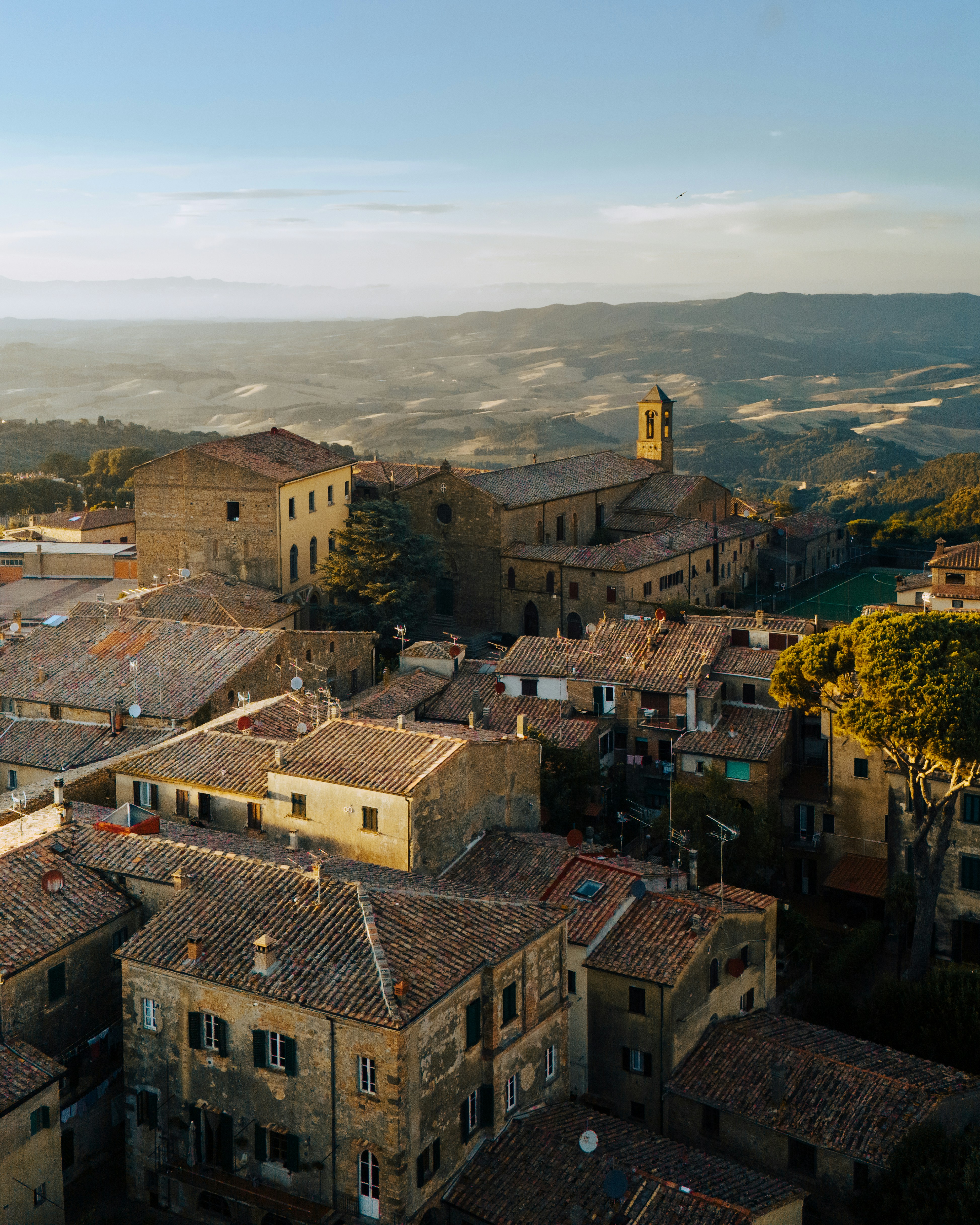 Aerial view of a quaint Tuscan village, showcasing terracotta rooftops and historic buildings nestled against a backdrop of rolling hills.
