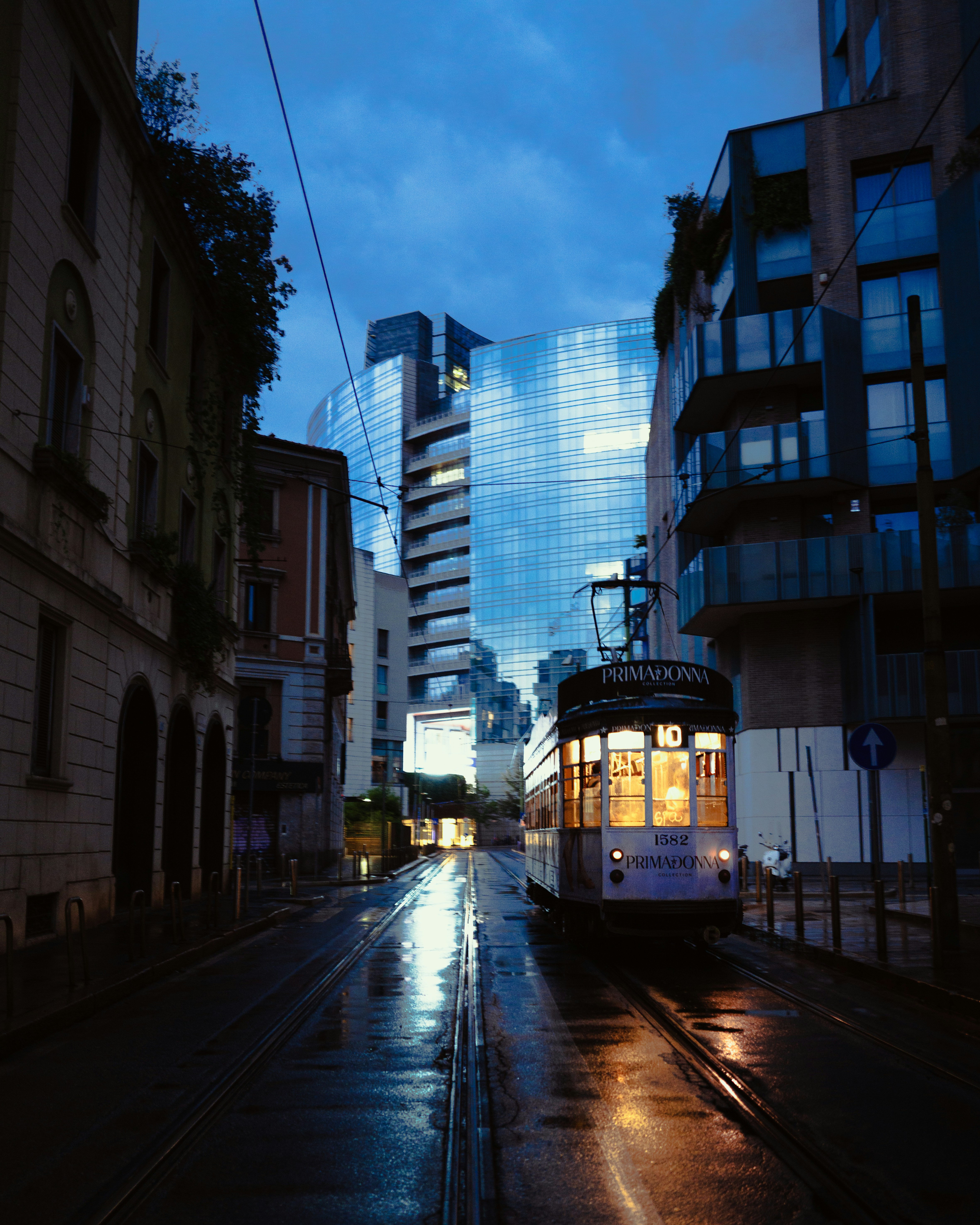 Historic tram navigating a modern urban landscape, illuminated against a backdrop of reflective glass buildings after rain.