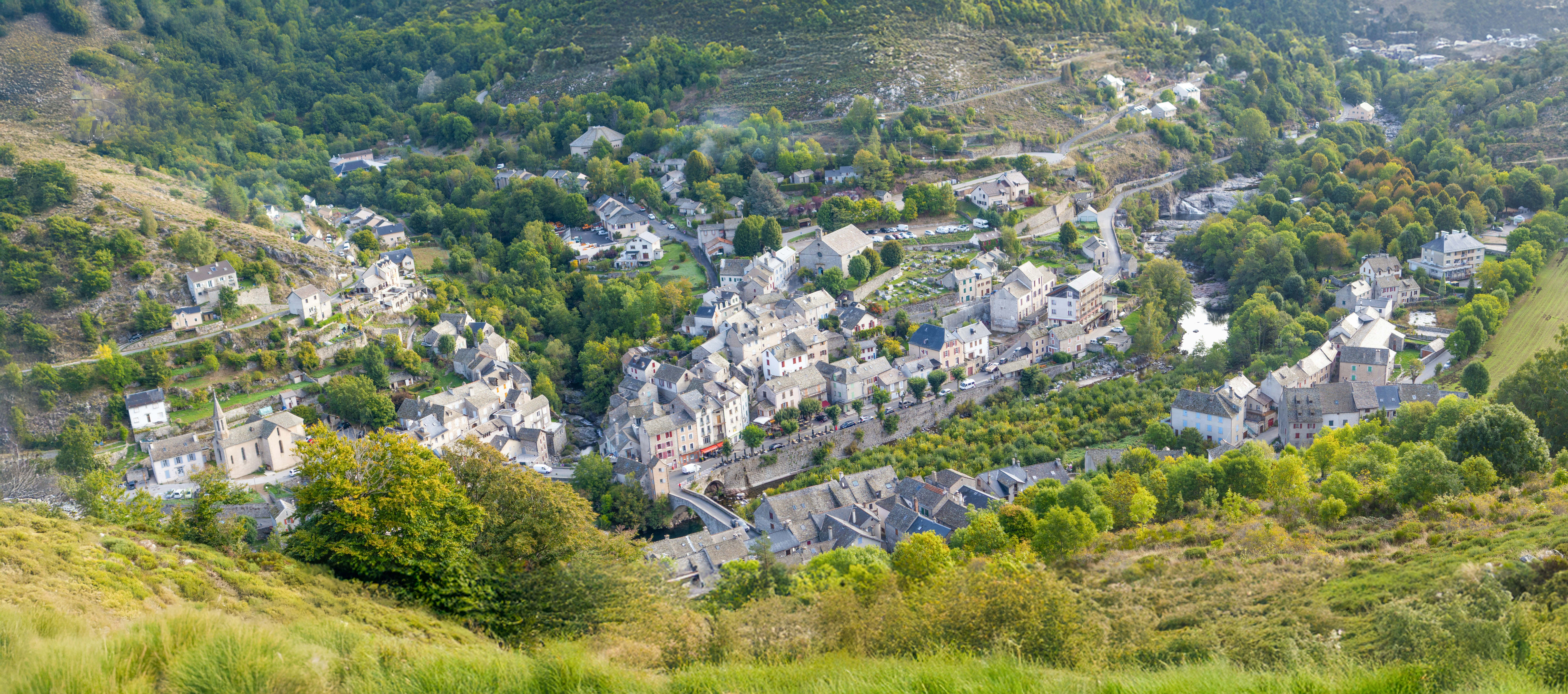 Aerial view of a quaint village surrounded by lush greenery and rolling hills, showcasing the harmony between architecture and nature.