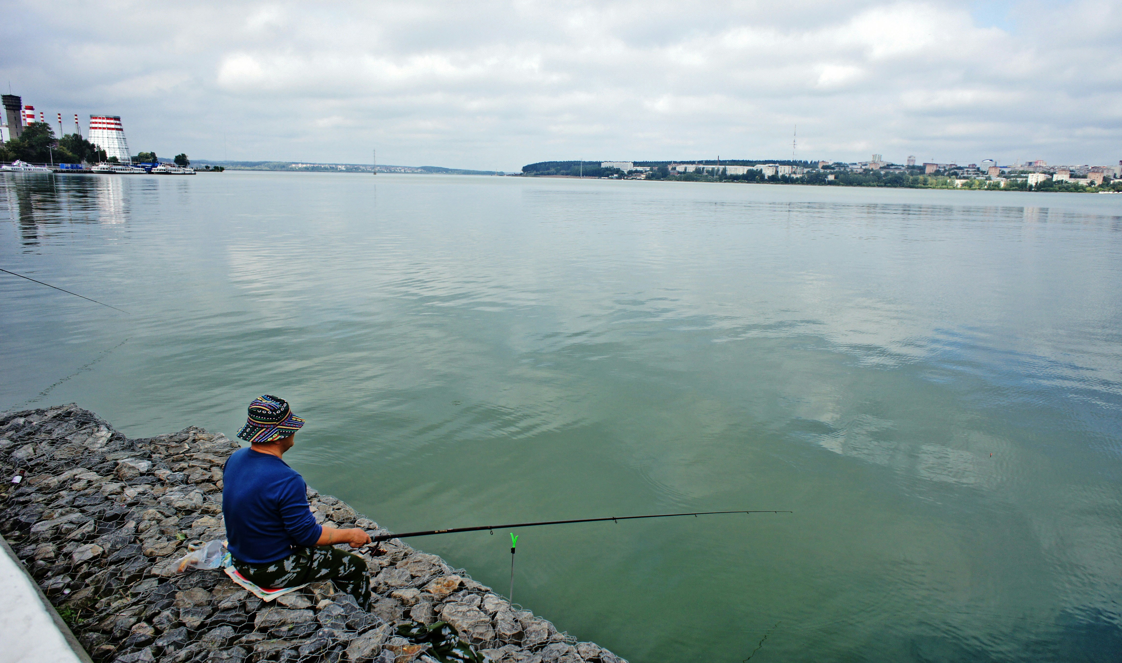 SONY DSC | Man fishing from rocky shore beside calm water
