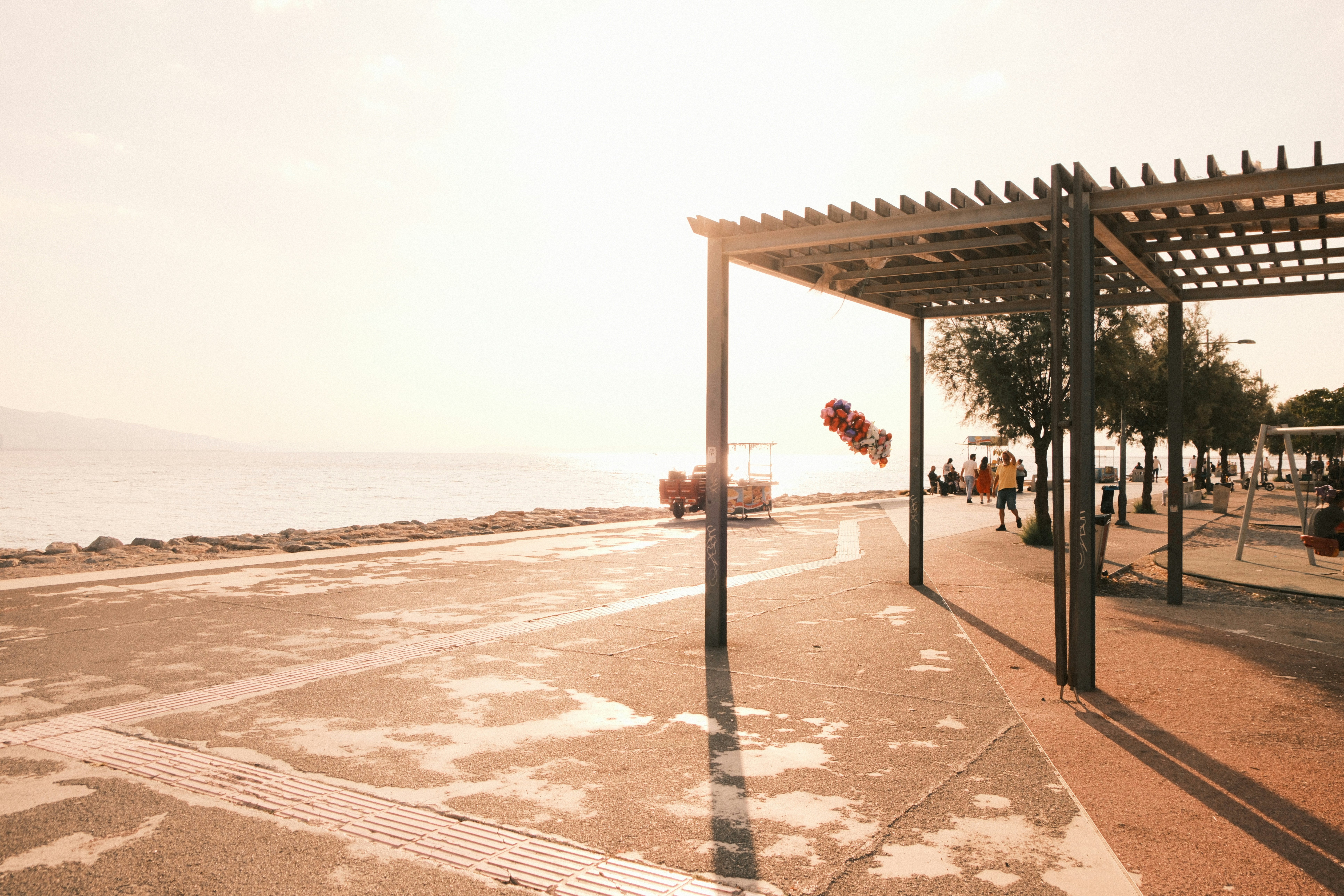 Sunny promenade with pergolas and distant people.