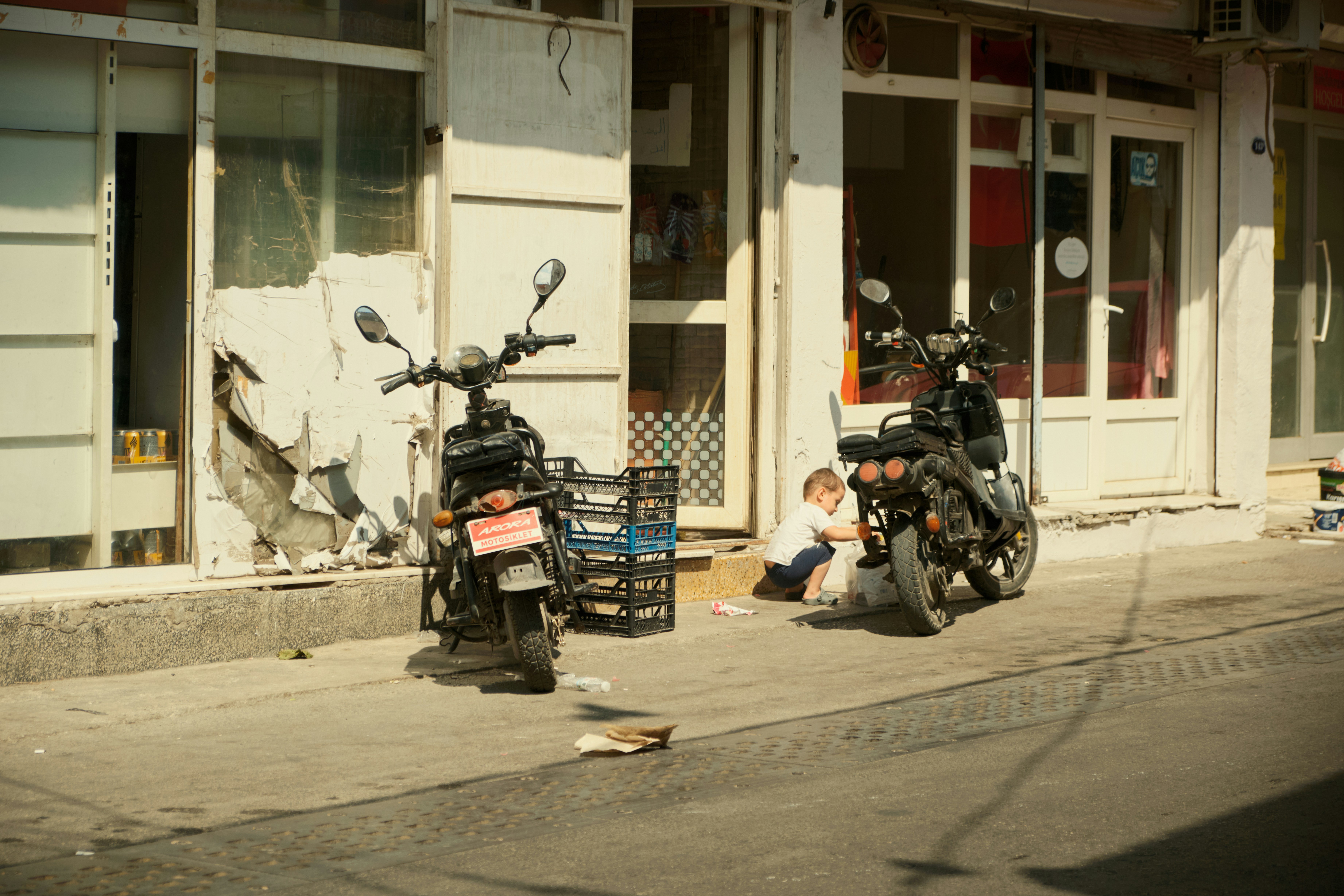Two motorcycles parked on a sidewalk with people sitting.