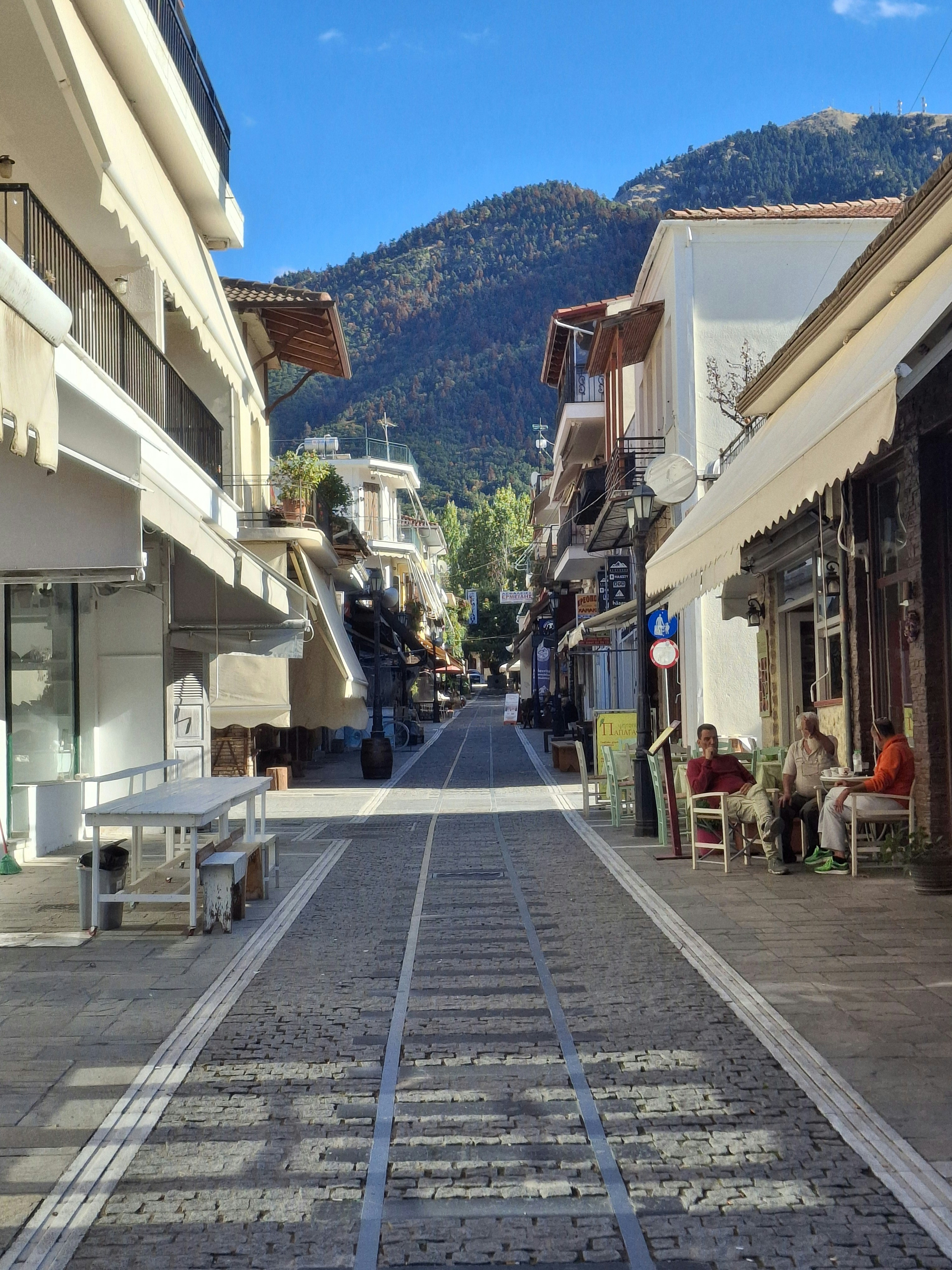 Street with shops and people in front of mountains.